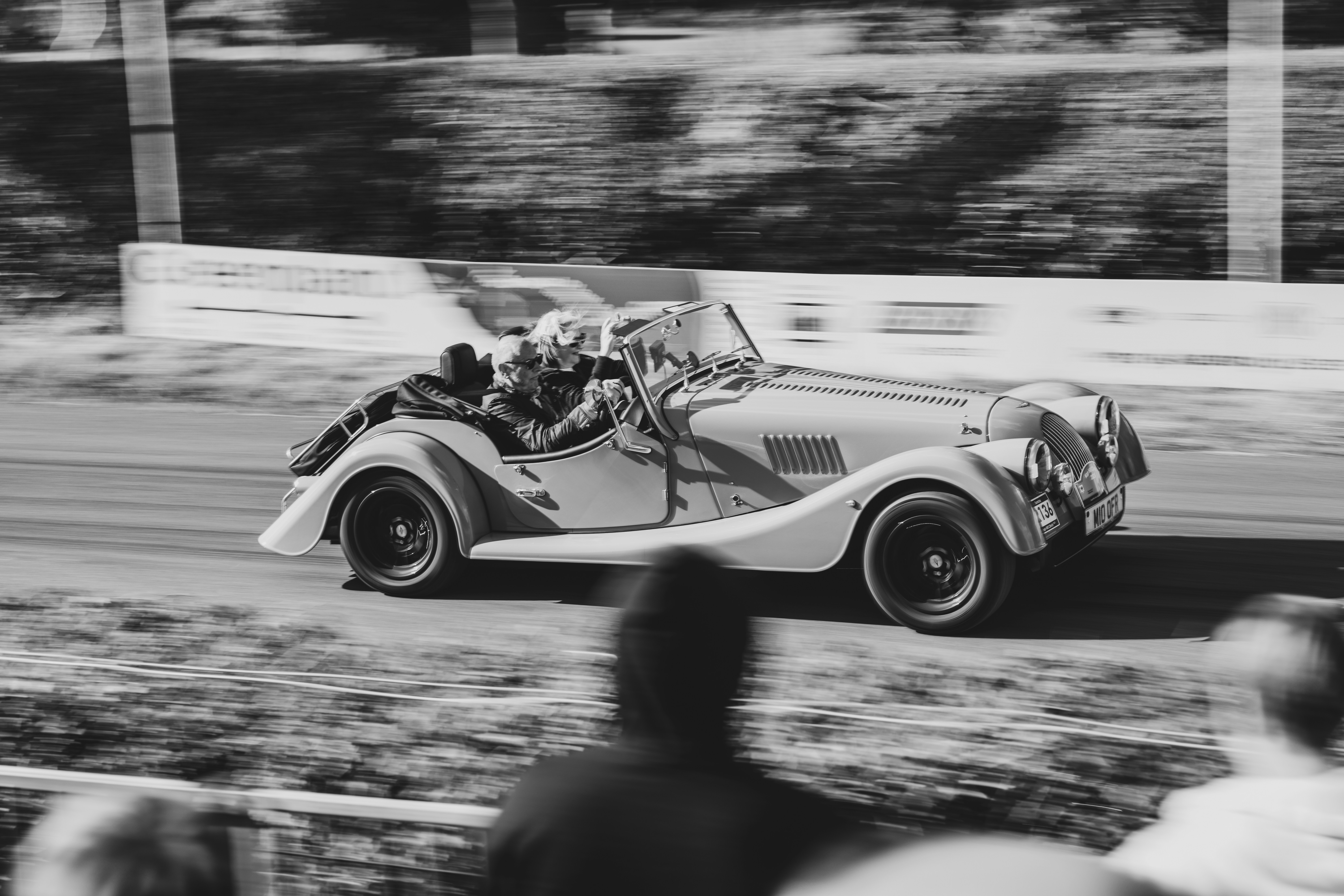 Dust and Chrome: a 1930s roadster rockets past blurred spectators in monochrome