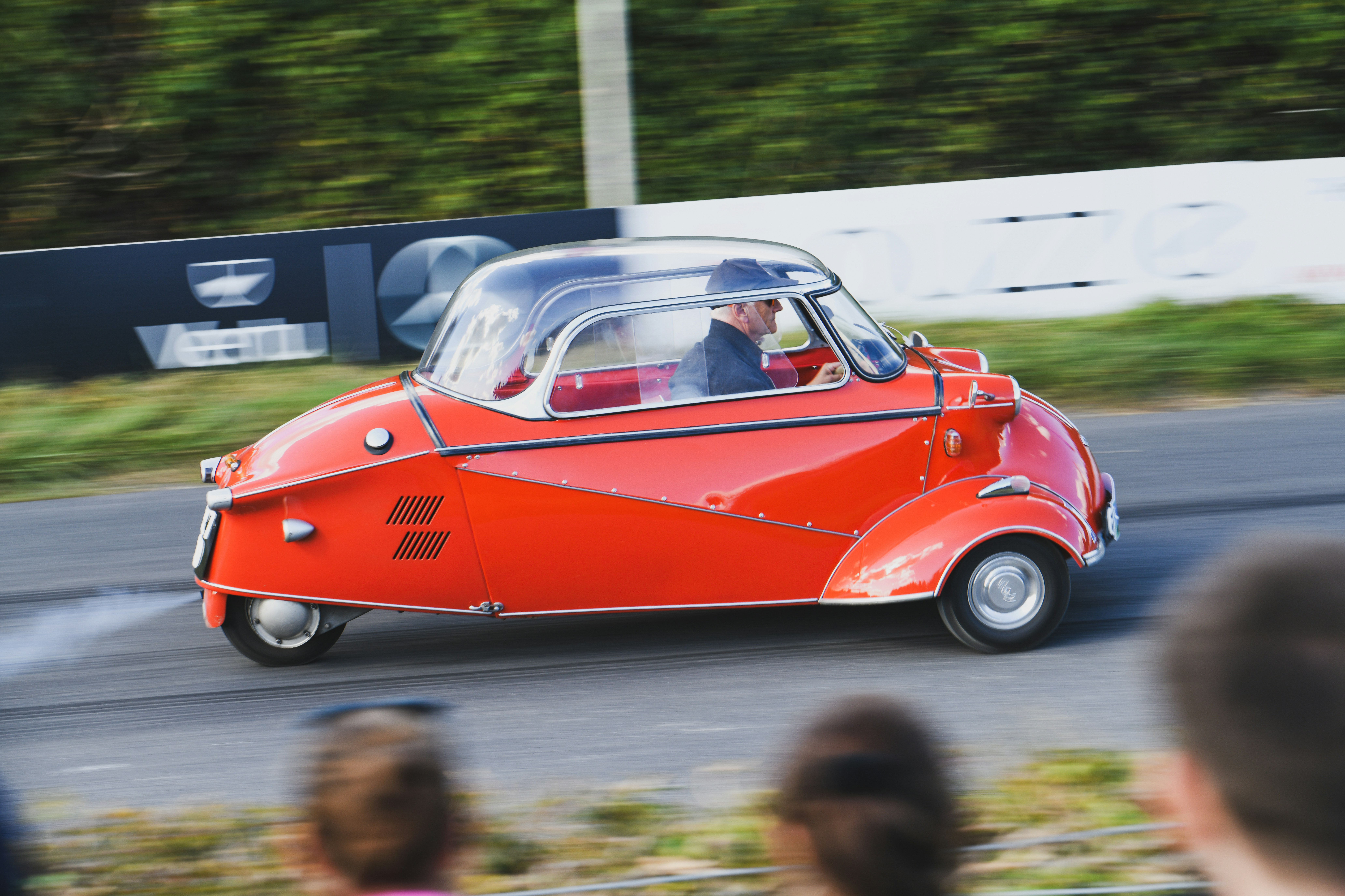 A vintage red microcar driving on a road.