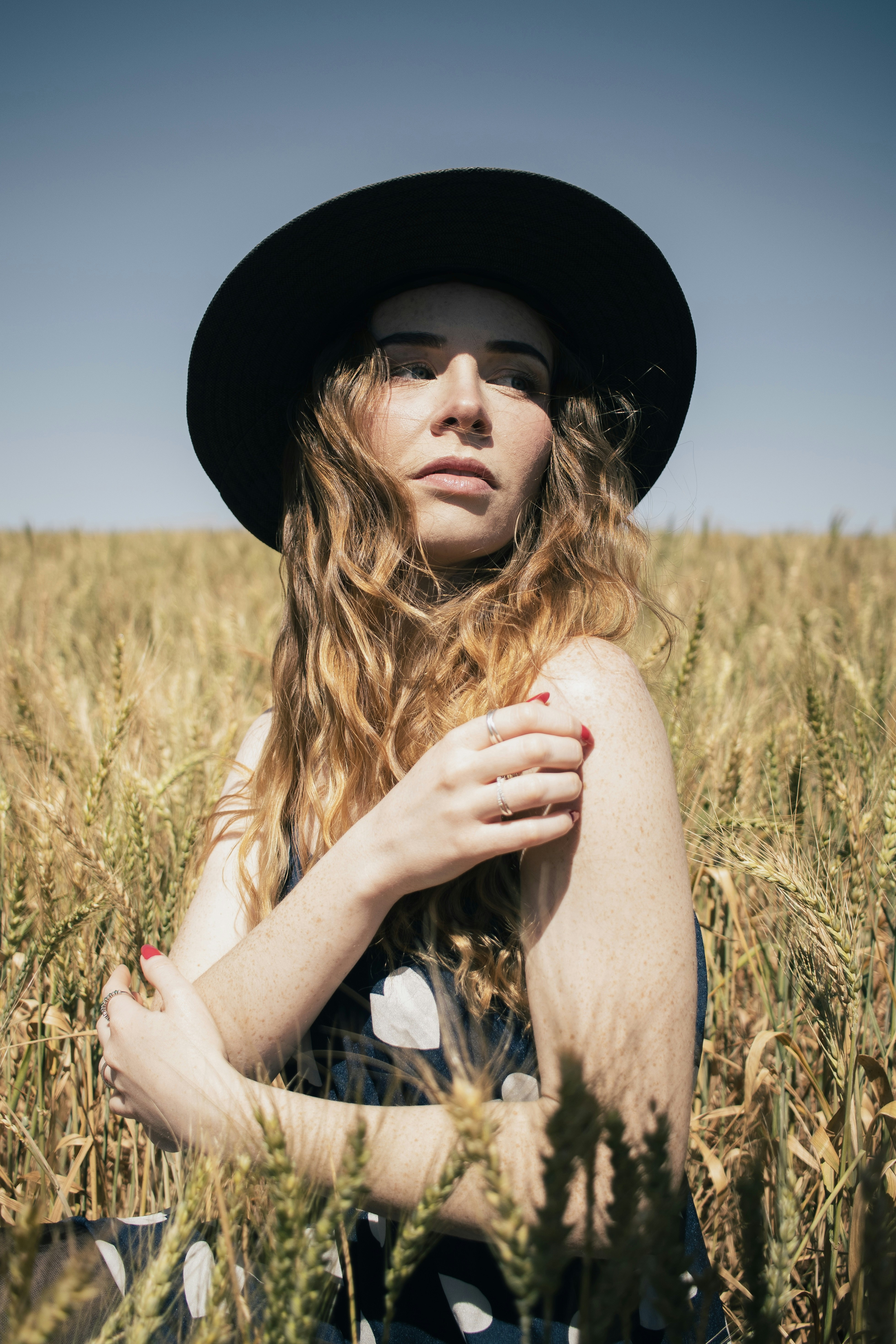 Woman in hat stands in a golden wheat field.