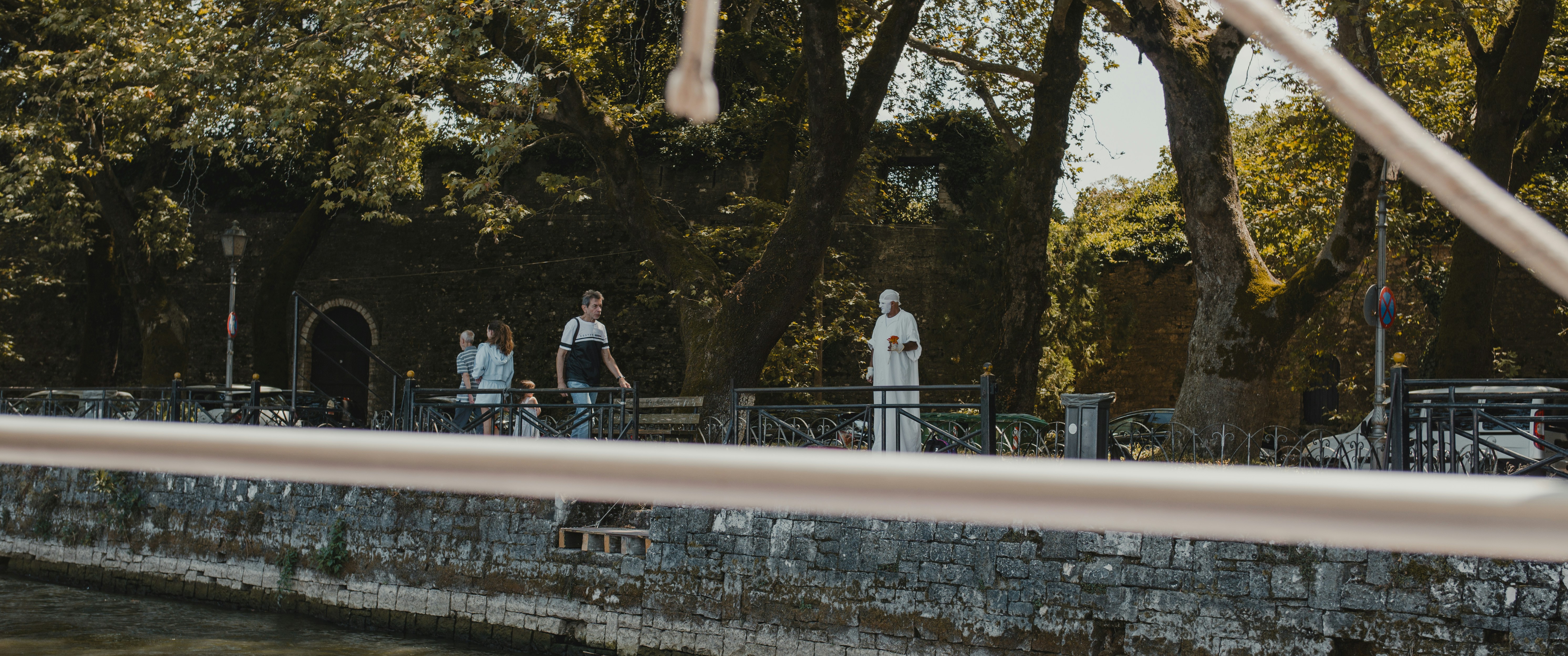 People walk along a tree-lined waterfront promenade.