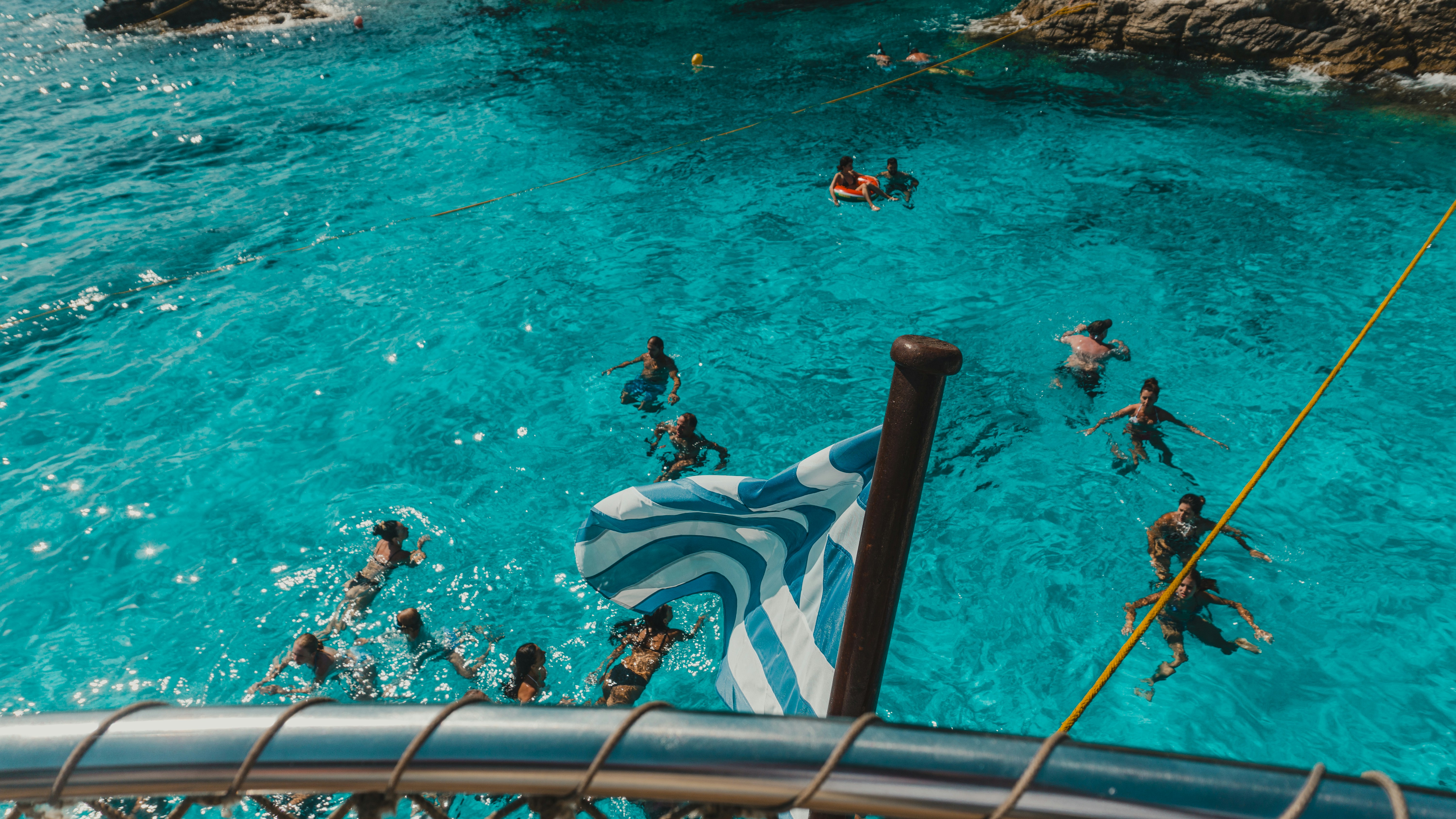 People swimming in clear turquoise water near rocky shore.