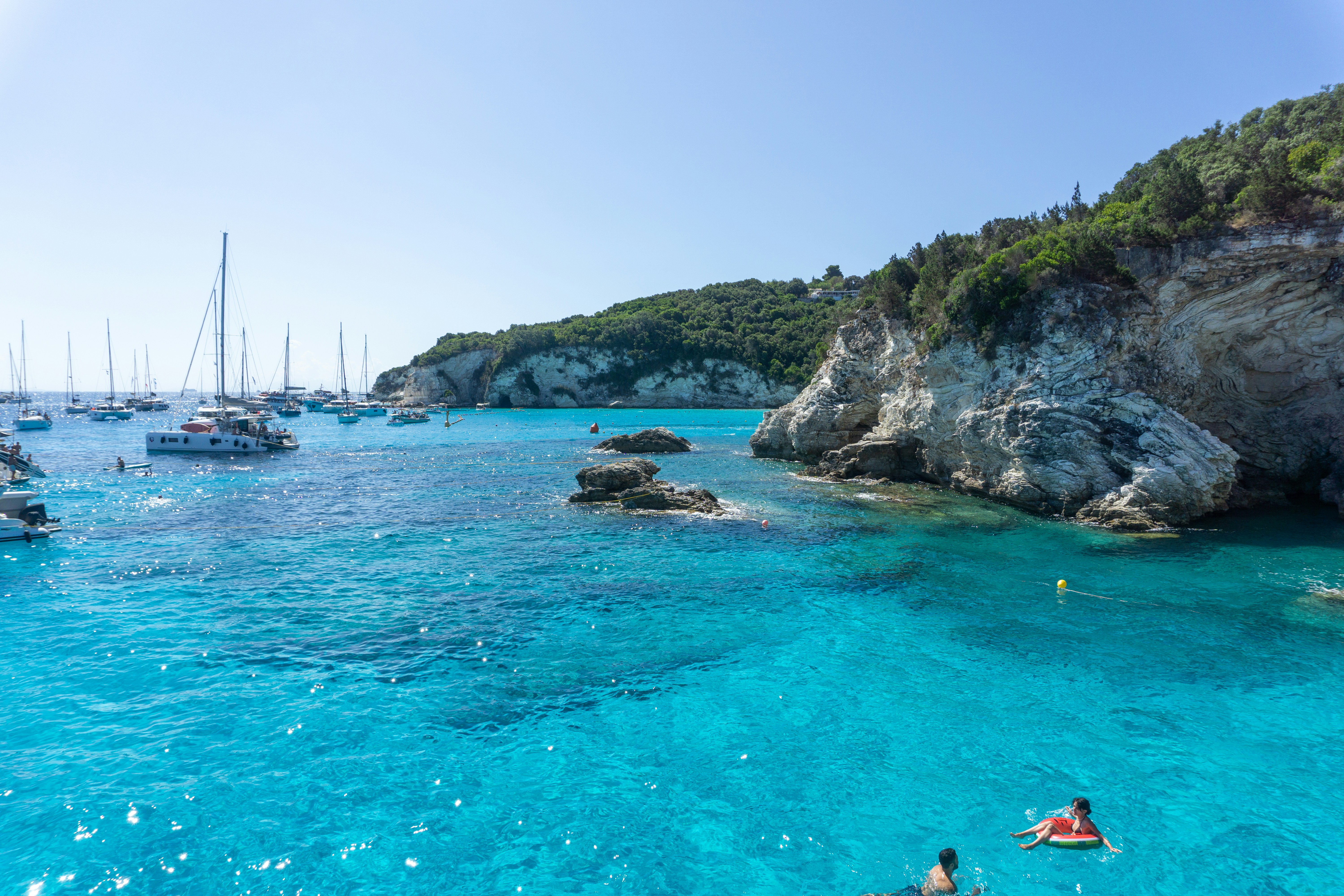 Boats anchored in a clear turquoise bay with rocky cliffs.