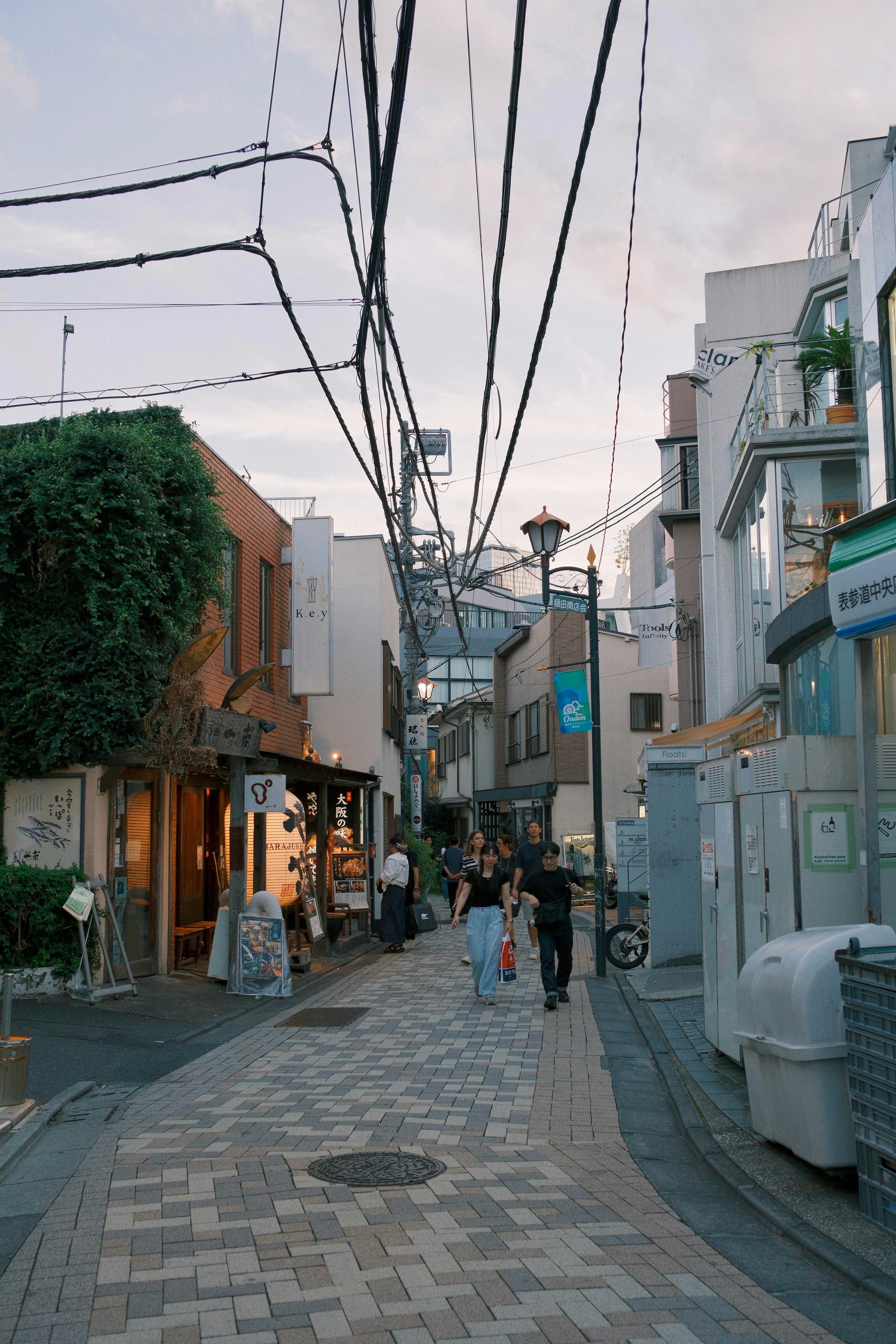 People walk down a narrow street with overhead wires.