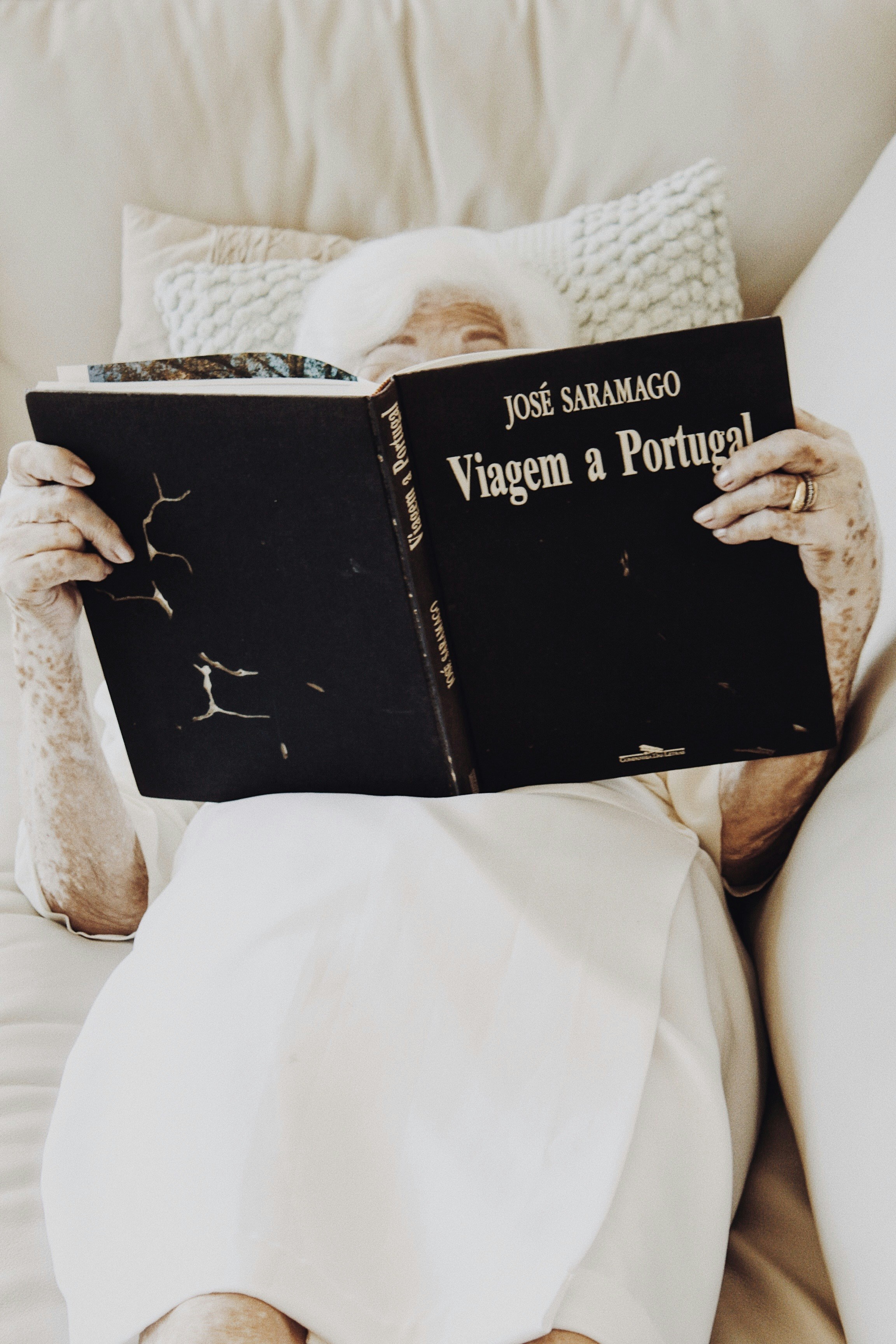 A grandmother accompanied by a good read | Elderly person reading a book on a couch.