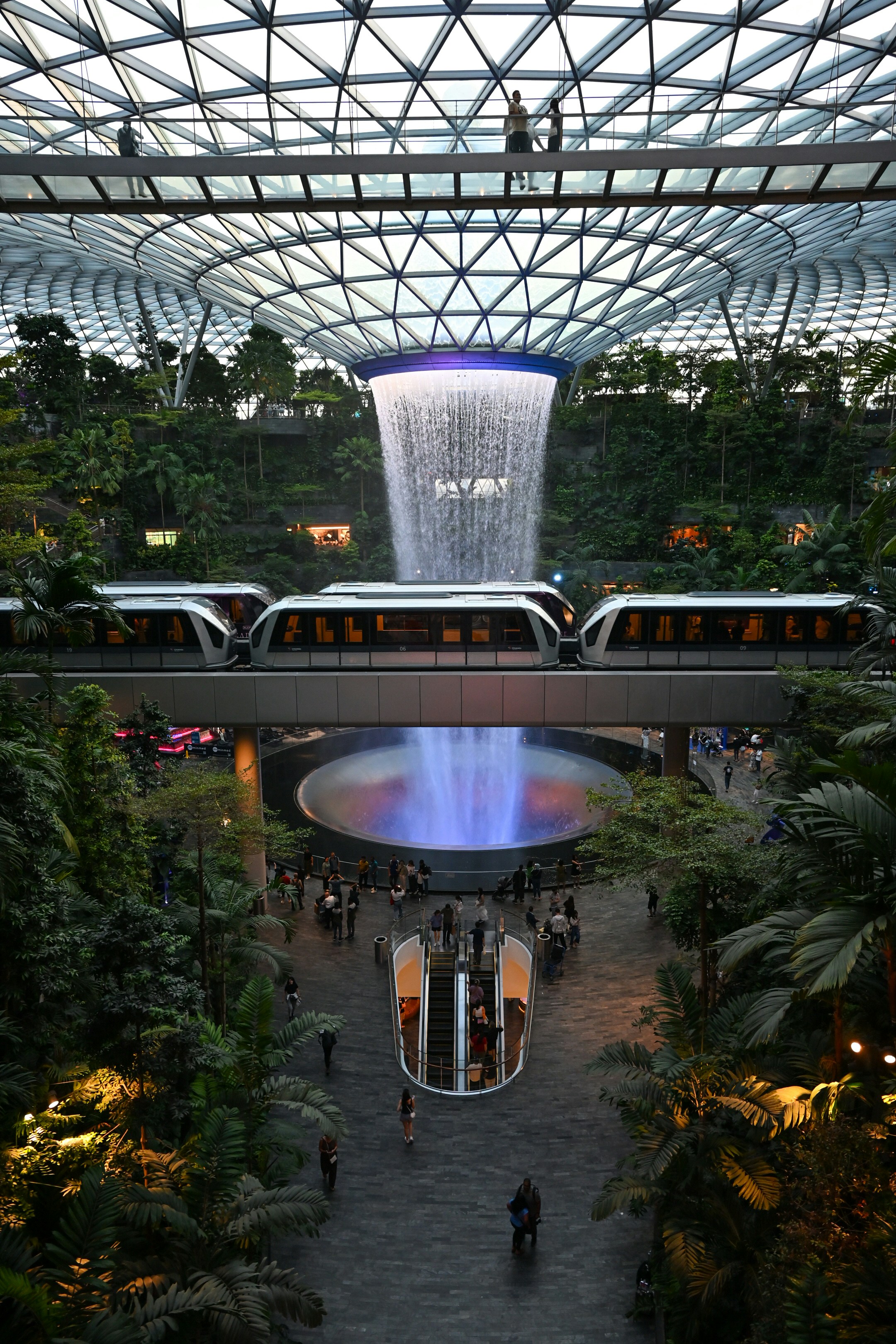 Indoor waterfall and monorail in a lush green atrium.