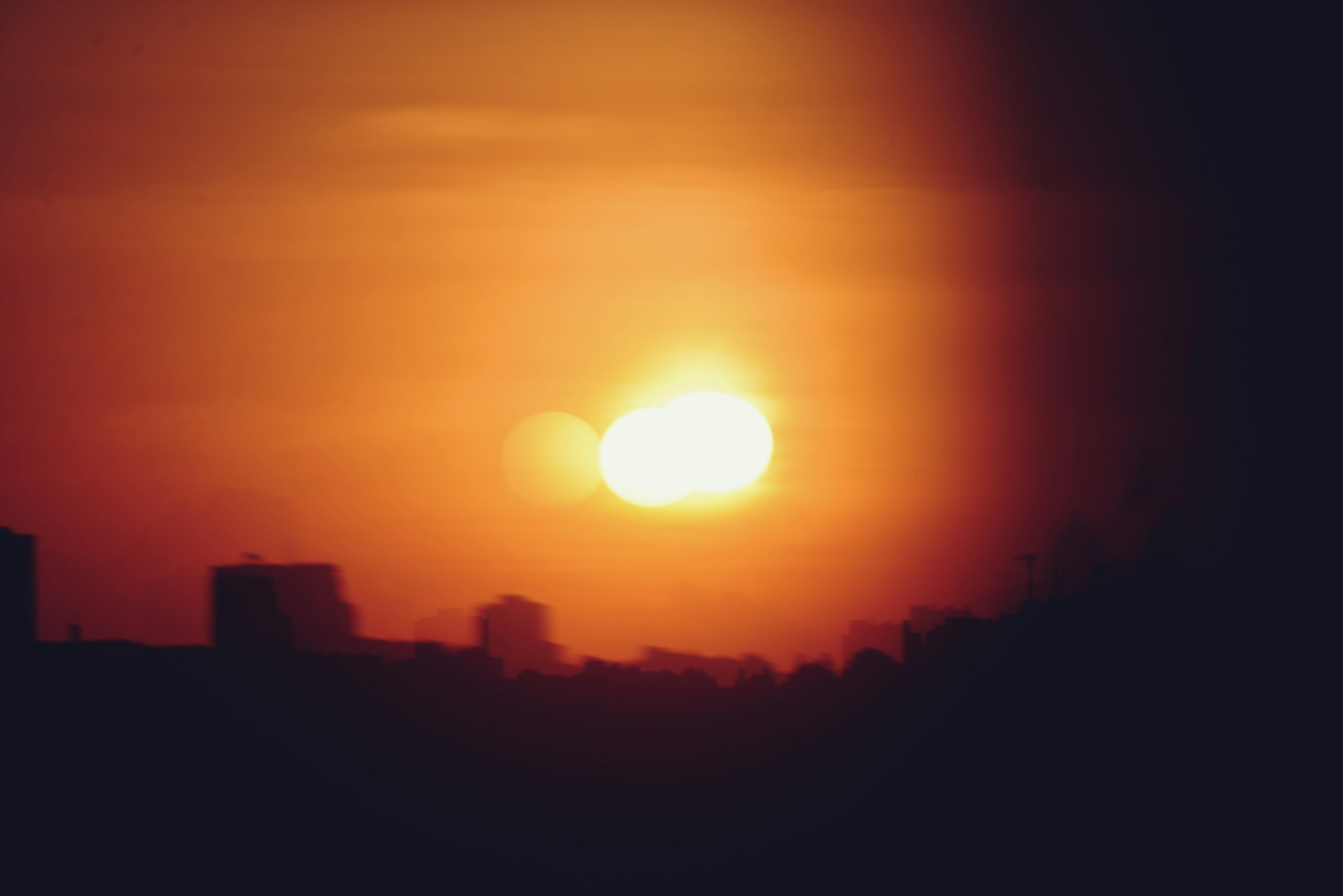 A hazy sun sets over a silhouetted cityscape.