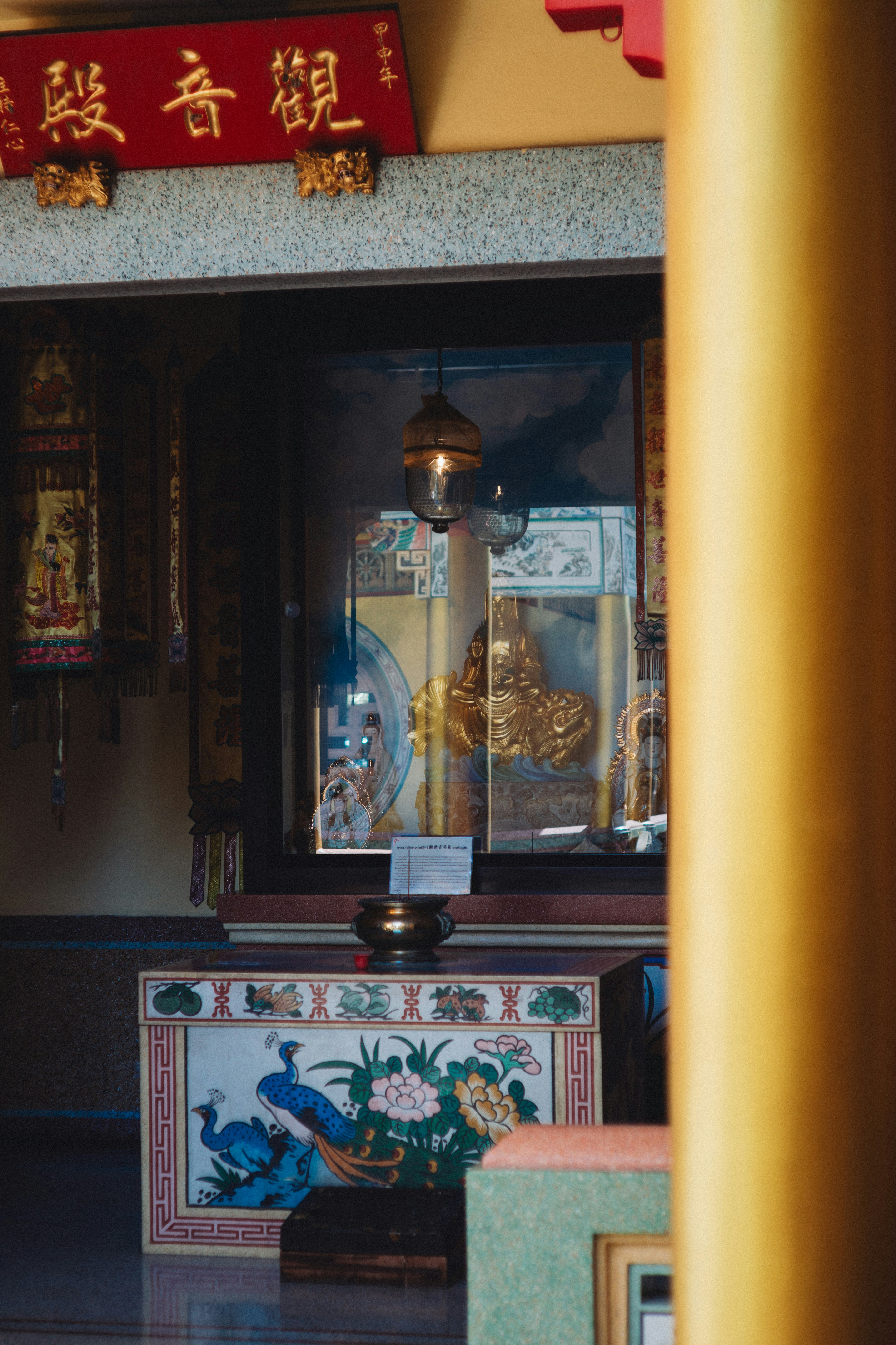 Intricately designed altar featuring peacock motifs, illuminated by a hanging lamp in a serene temple setting.