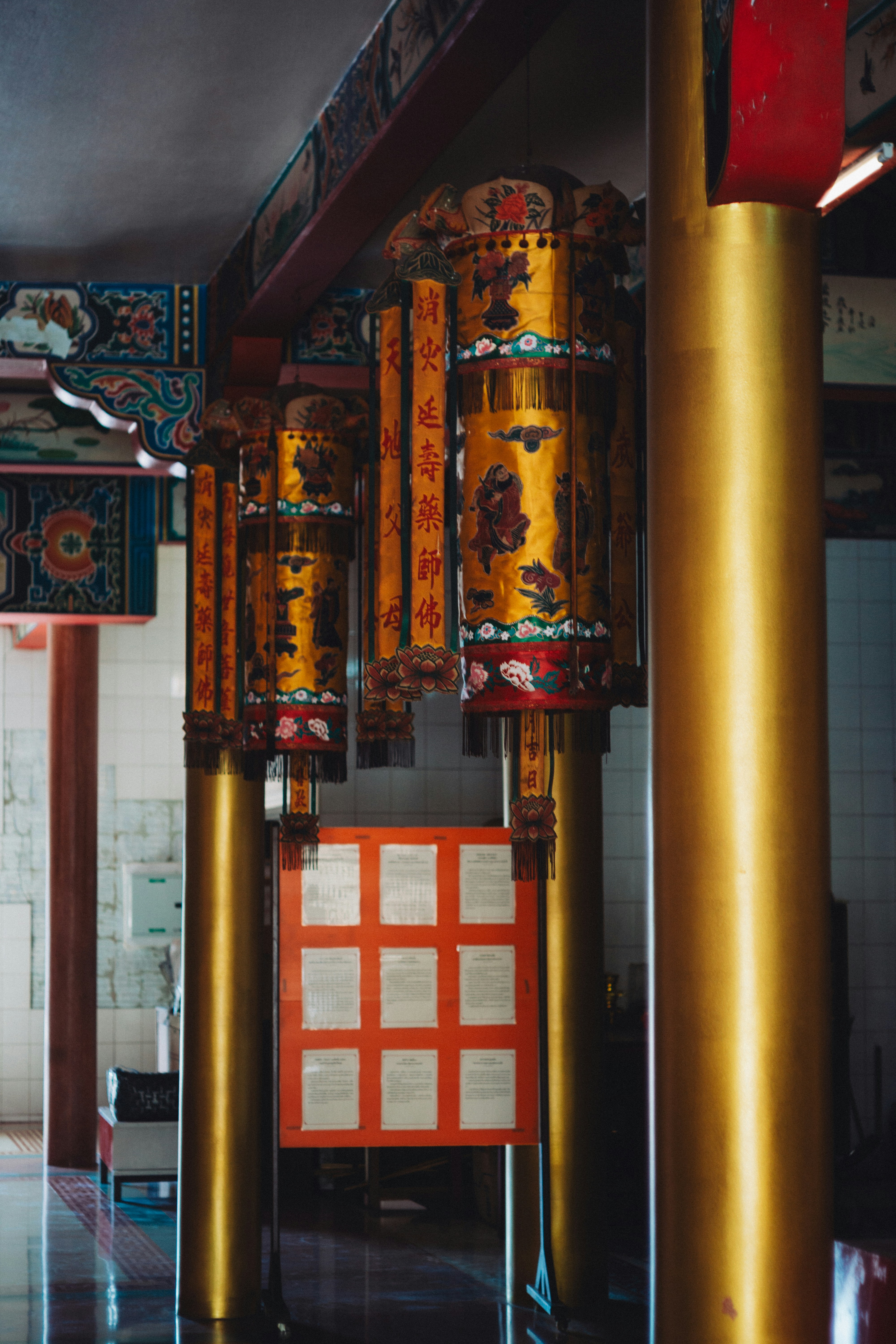Vibrant, intricately designed lanterns hang gracefully in a serene space, illuminated by soft light. A detailed notice board adds context to the cultural setting.