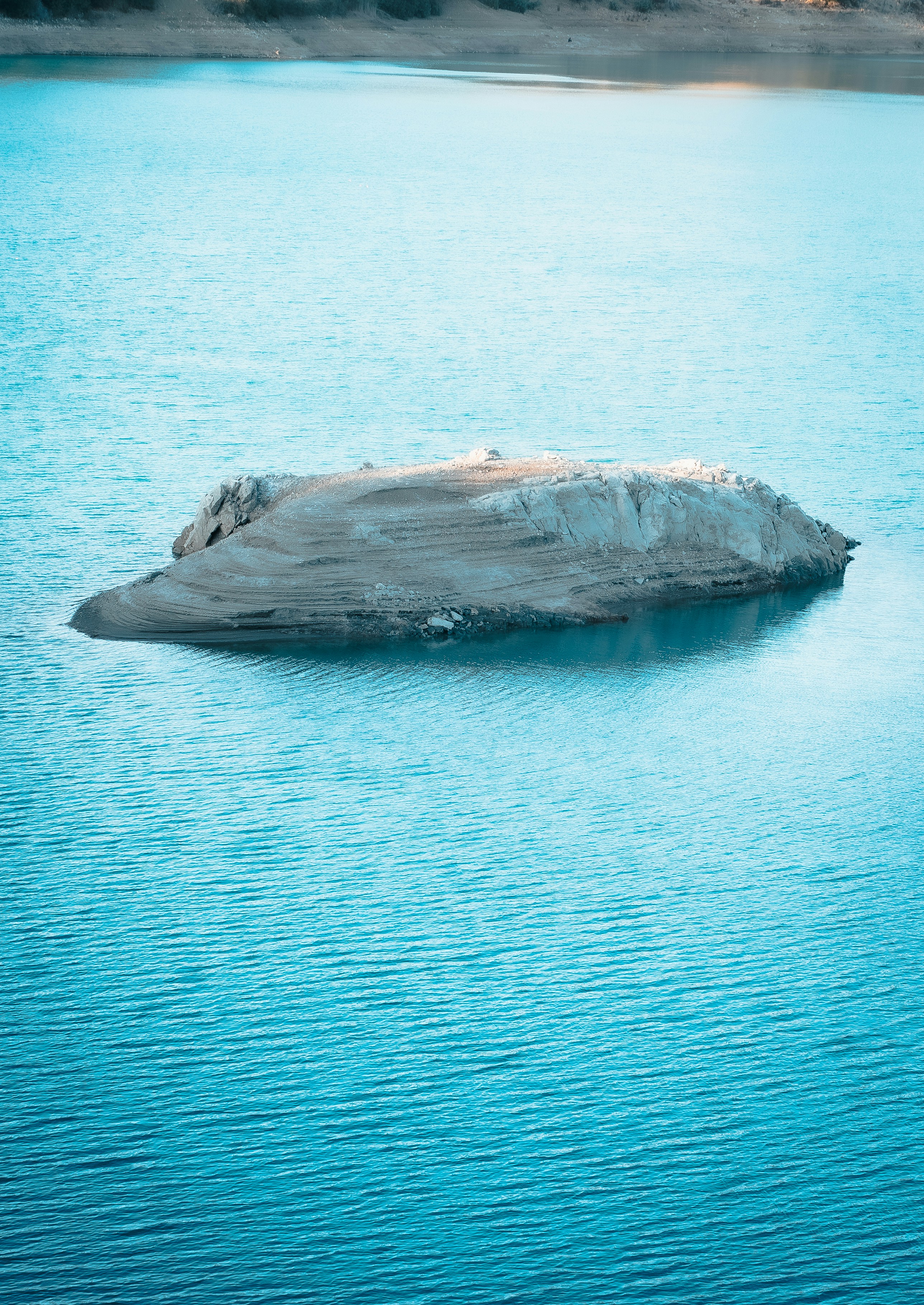 A solitary rock formation emerges from calm blue water.
