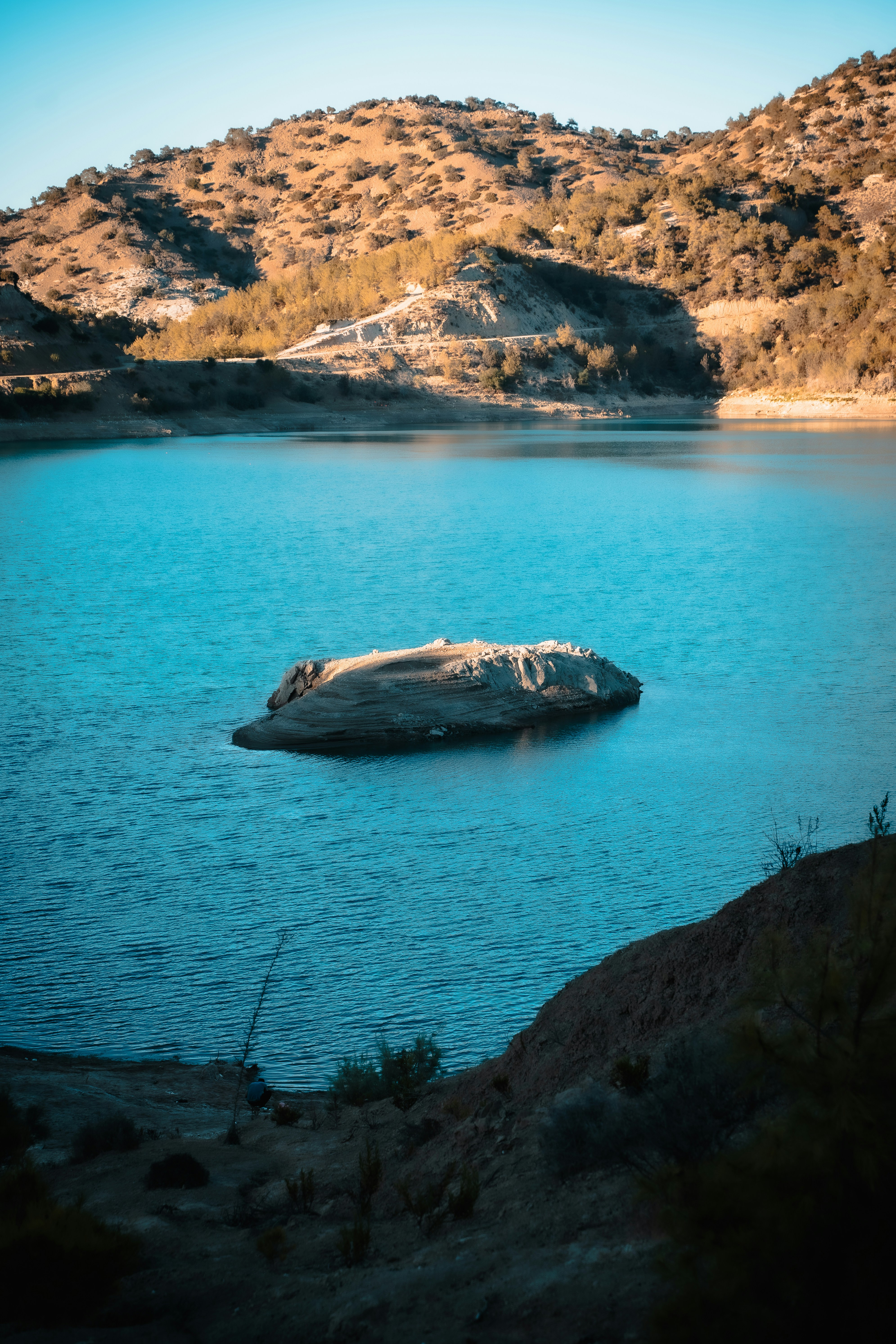 Rocky island in a large blue lake with hills.