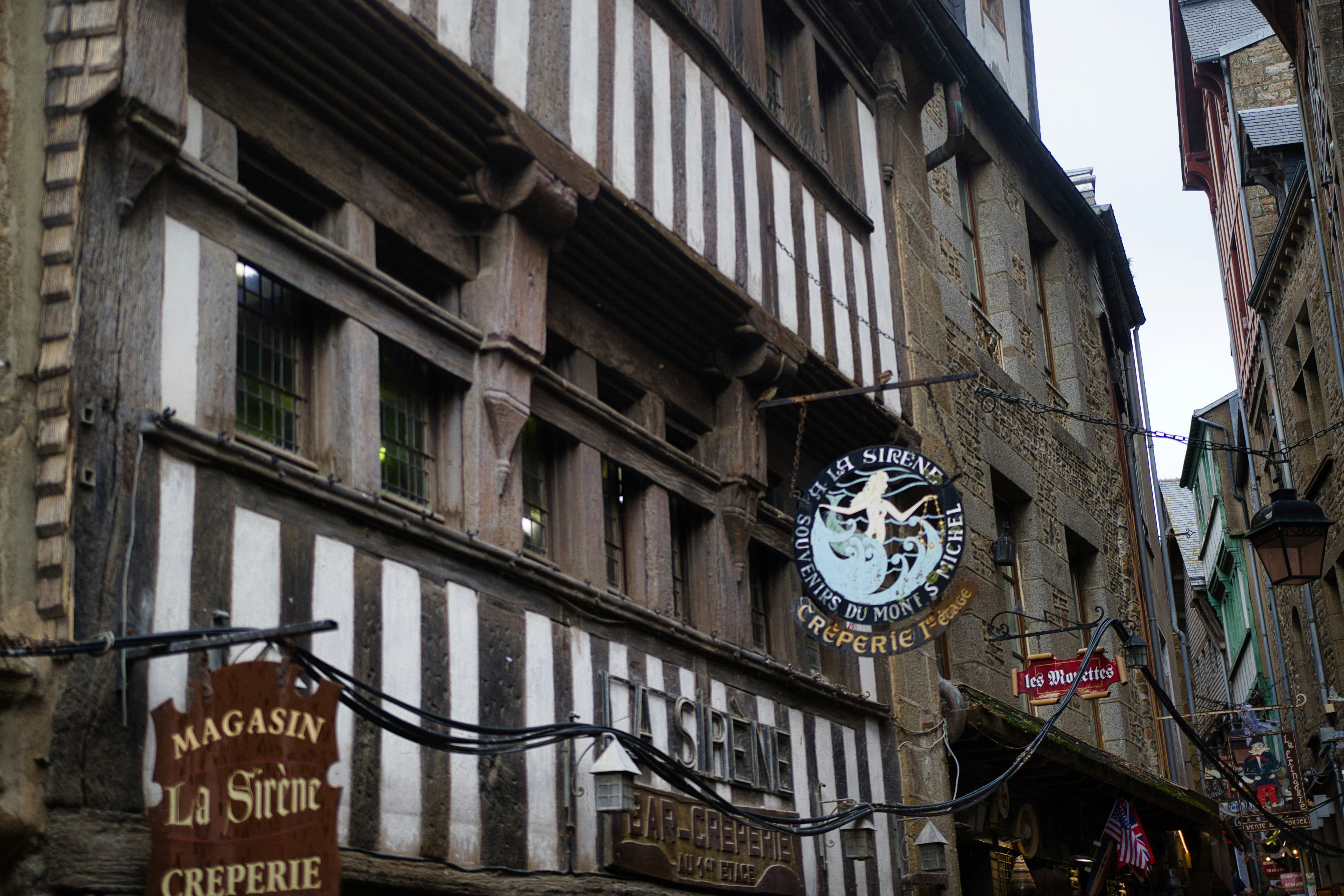 Charming half-timbered buildings line a narrow street, showcasing a creperie sign and traditional architecture. The scene evokes a sense of history and local culture.
