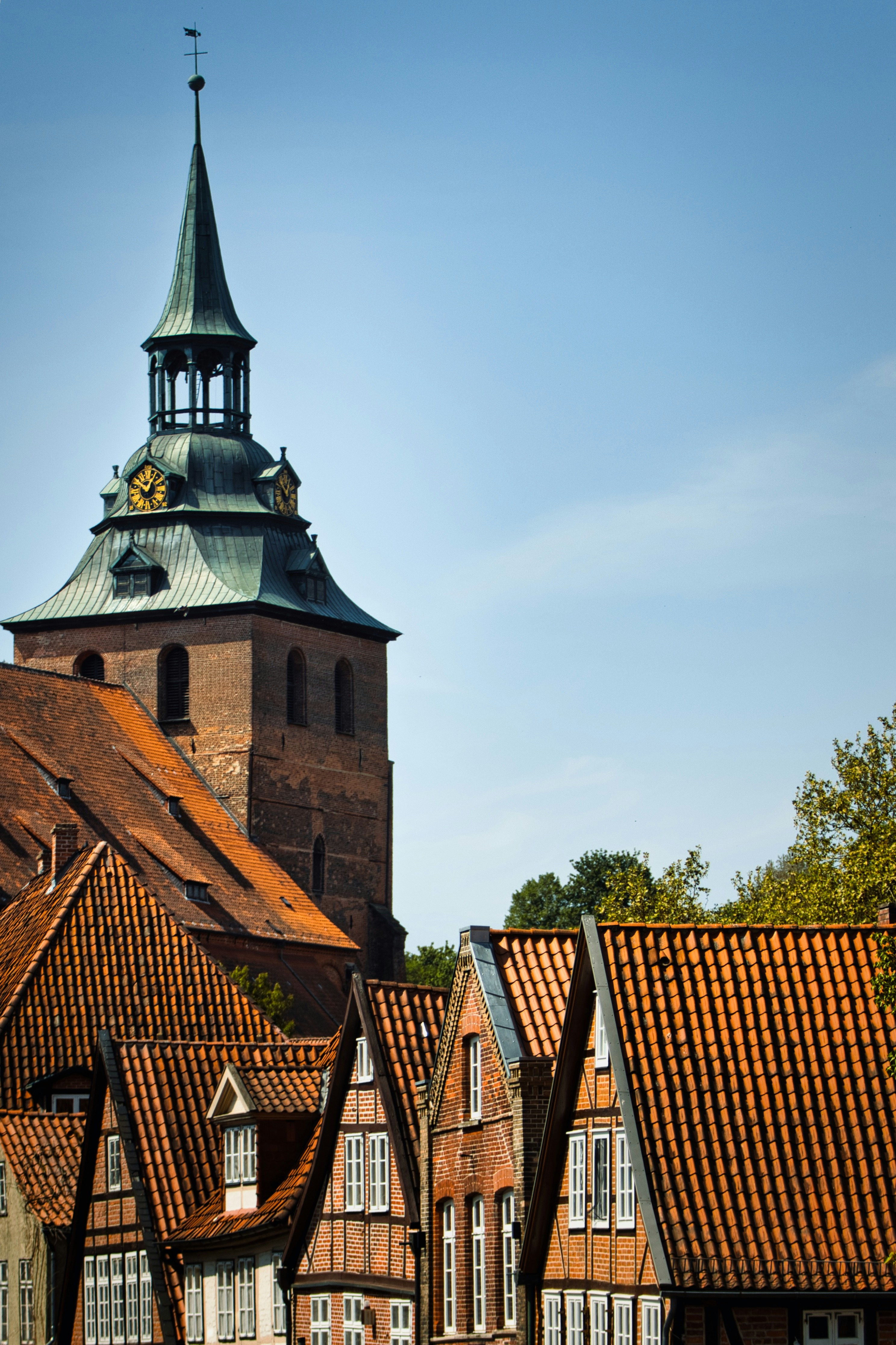 Historic brick church tower above tiled rooftops under blue sky.