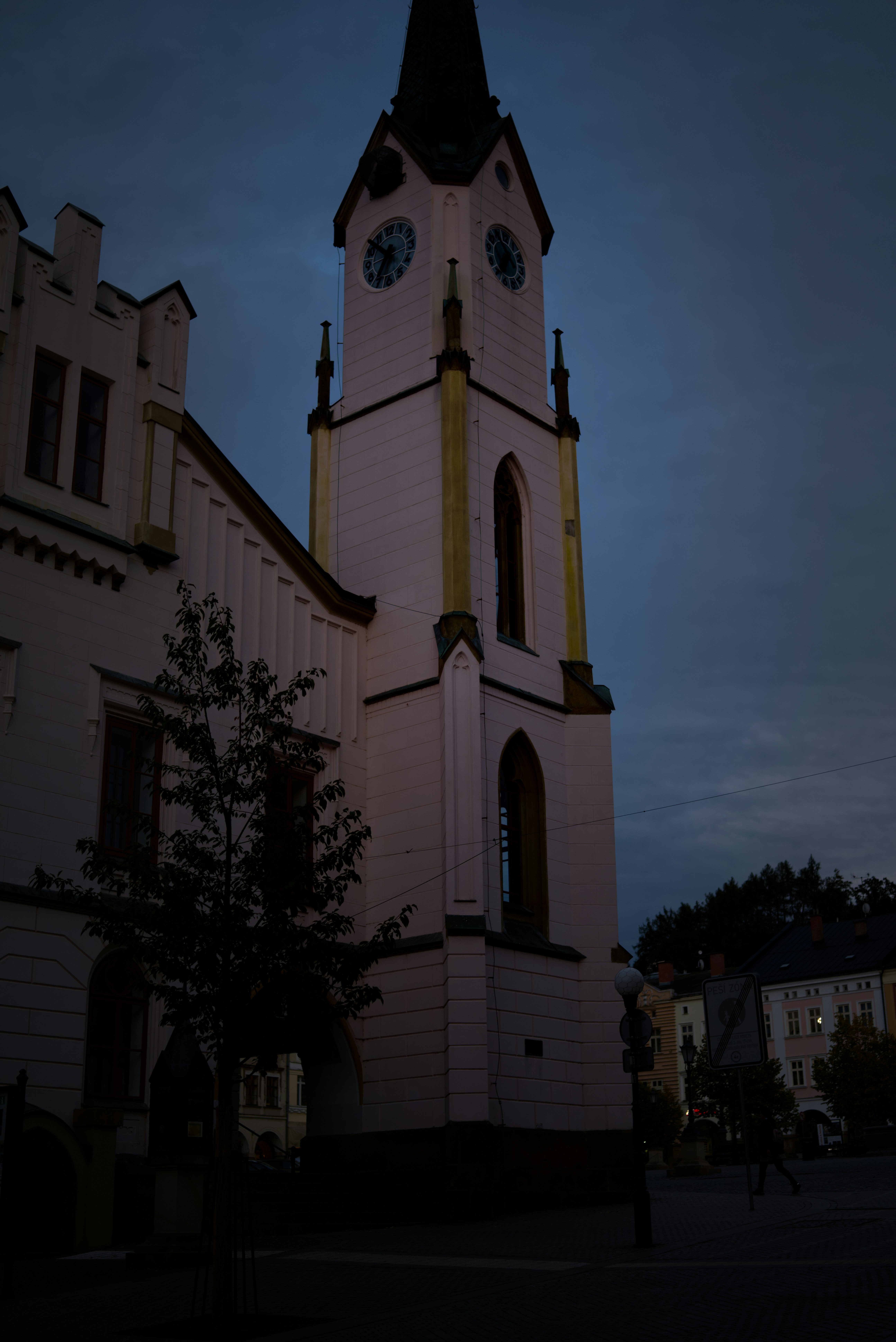 Historic clock tower stands against a twilight sky, casting a serene presence over the square. The architecture reflects a blend of styles, hinting at the town's rich history.