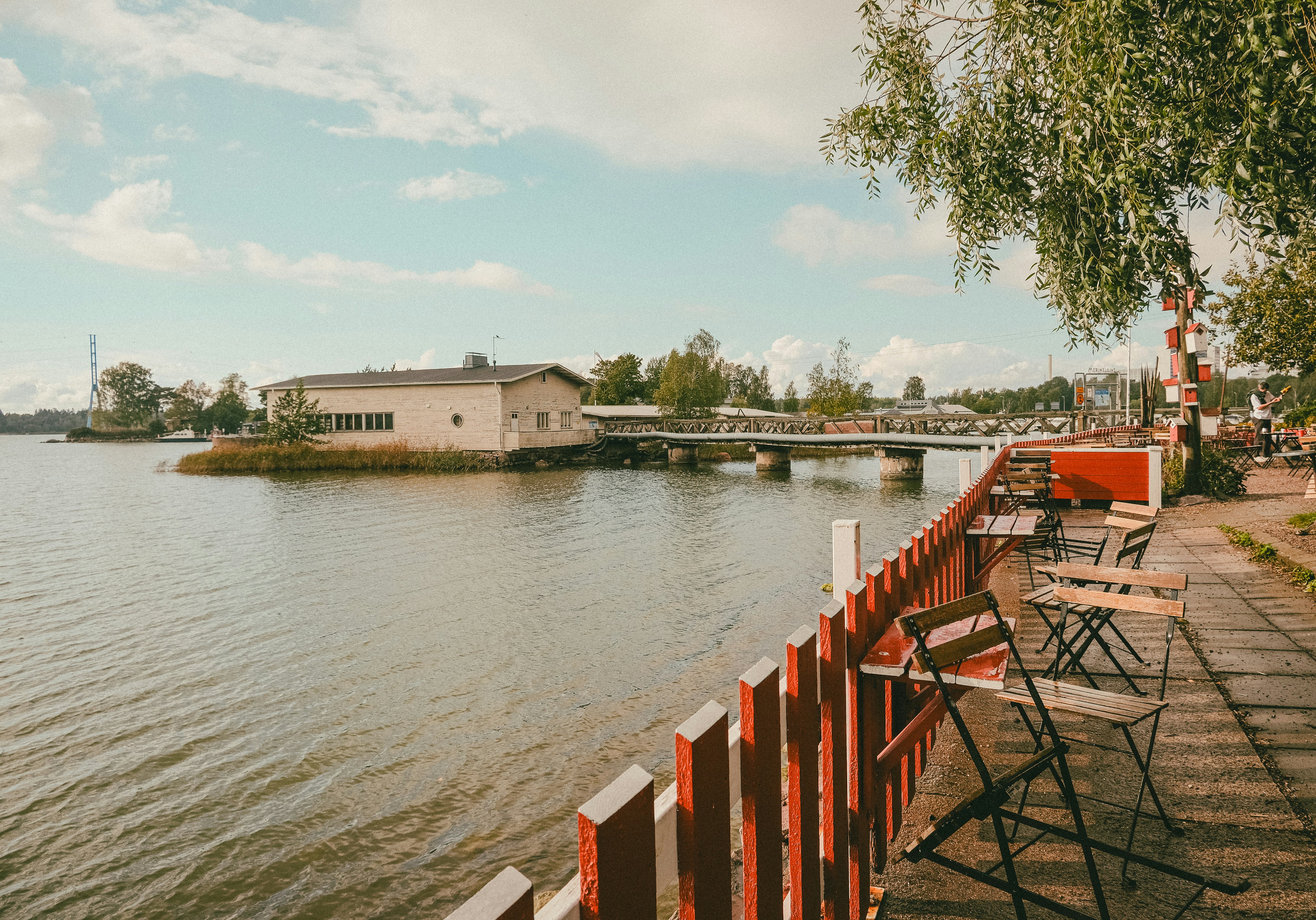 Cafe Regatta is located by the sea, close to Sibelius monument in Töölö. The traditional red cottage cafe has brought a part of Finnish countryside to the middle of Helsinki. | Waterfront cafe with tables and chairs overlooking water.