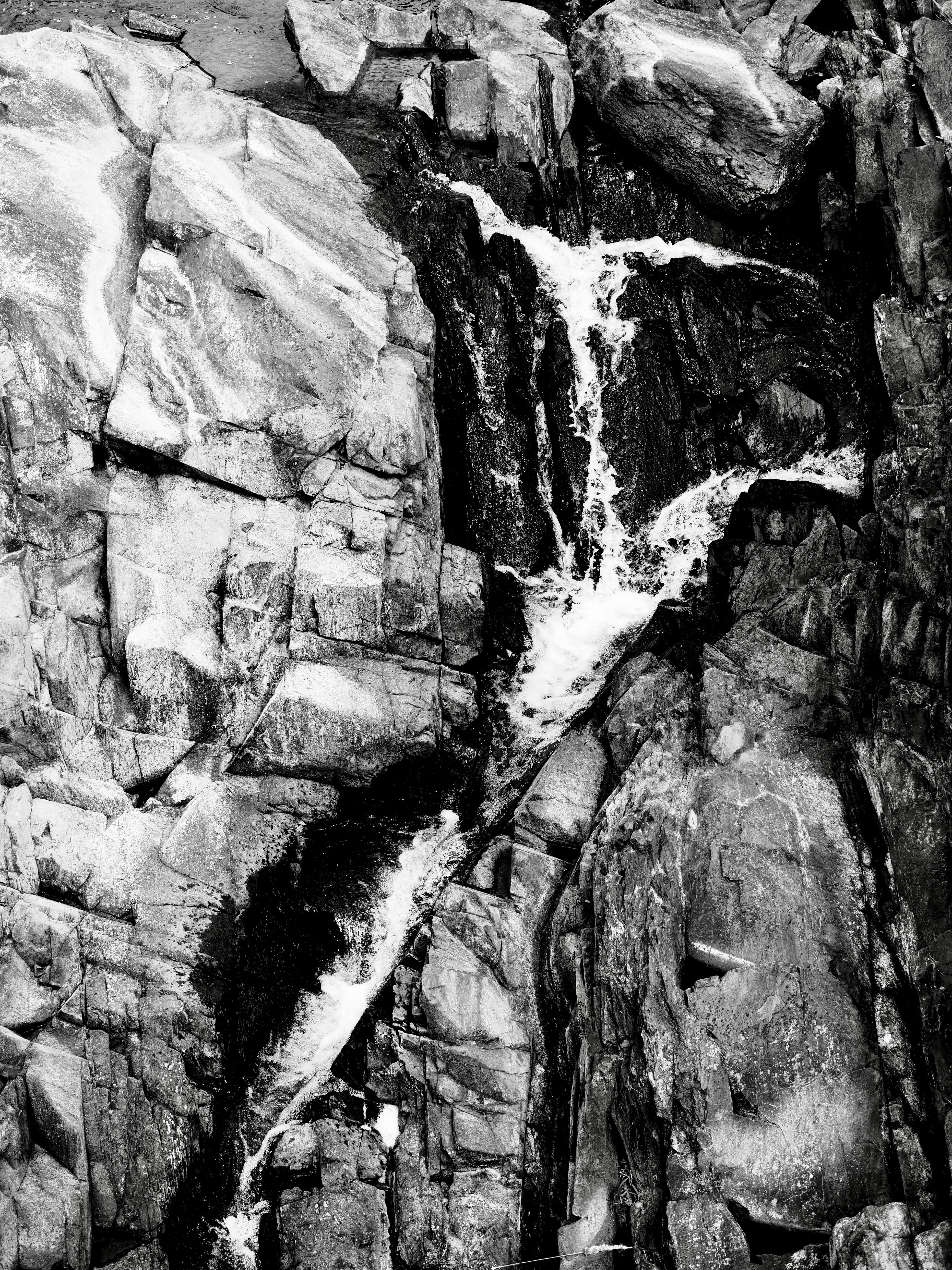 A small stream of water going over sone rocks | Water cascades down a rocky cliff face.