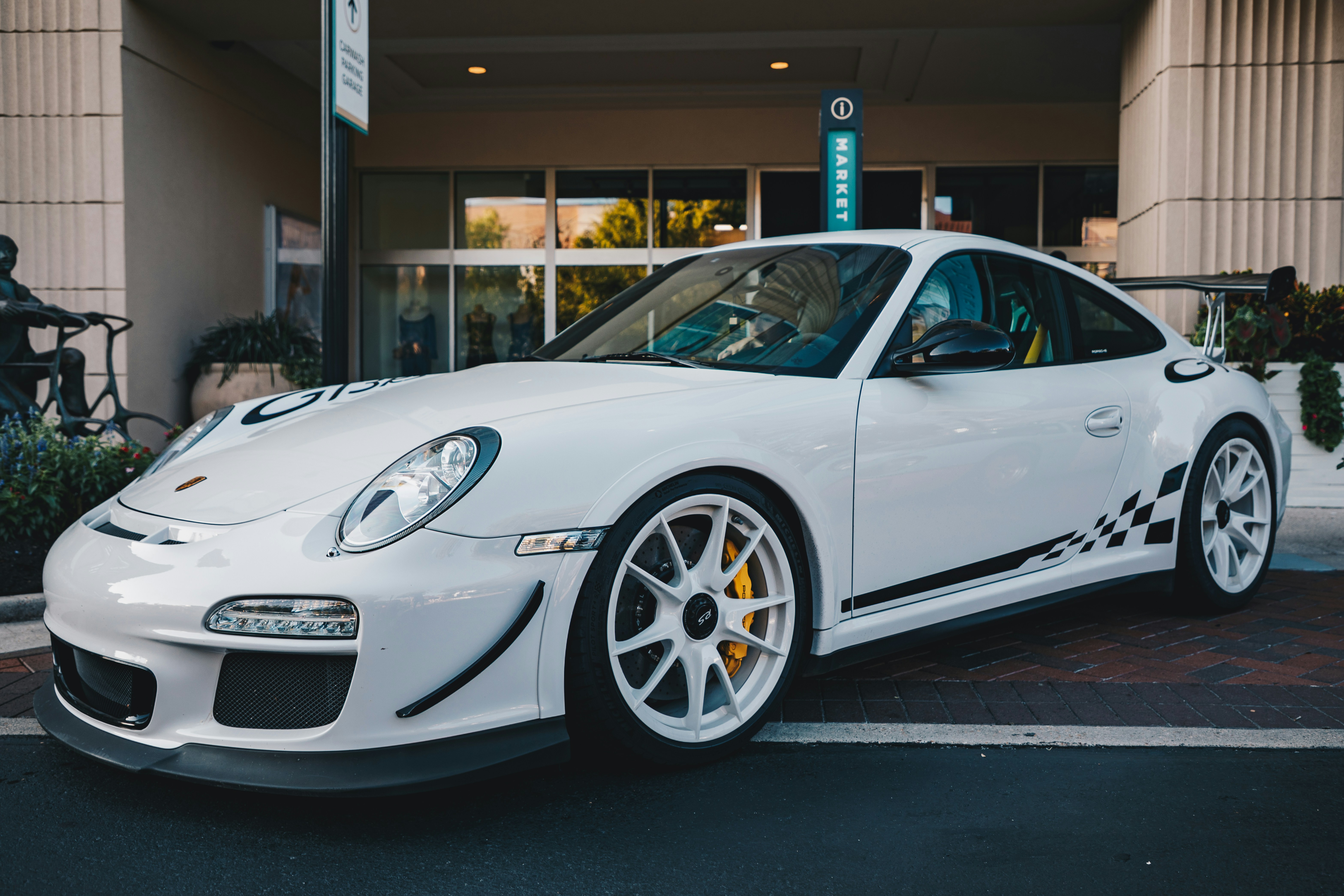 Sleek white Porsche sports car parked in an urban setting, showcasing its aerodynamic design and striking wheels.