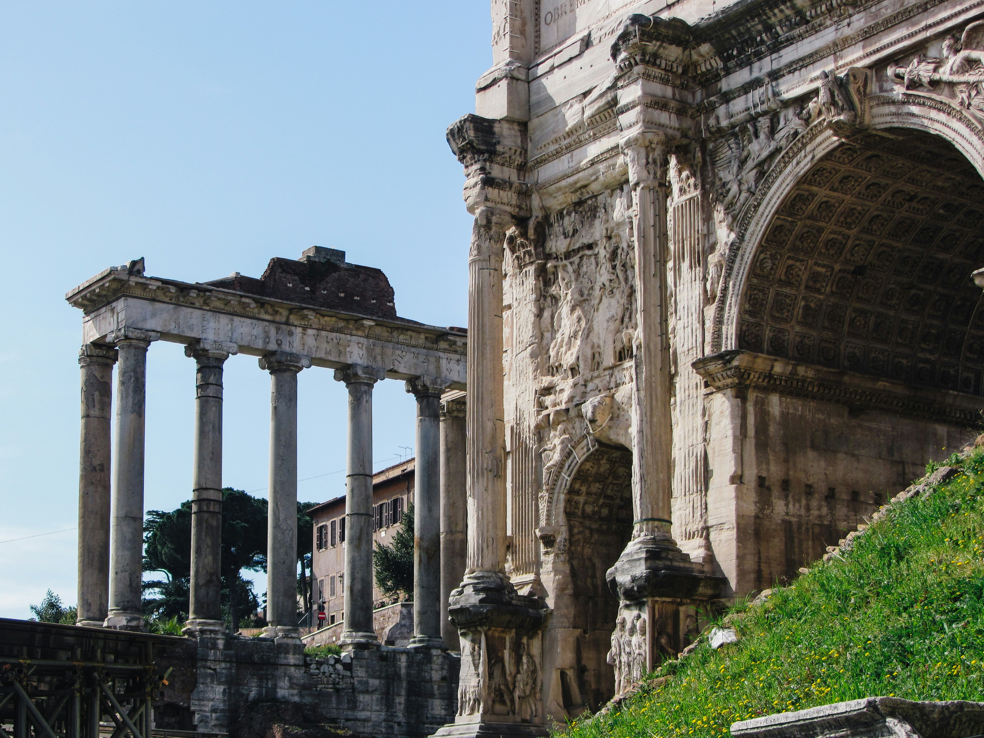 Ruins of the Roman Forum featuring towering columns and intricate archways amidst lush greenery.