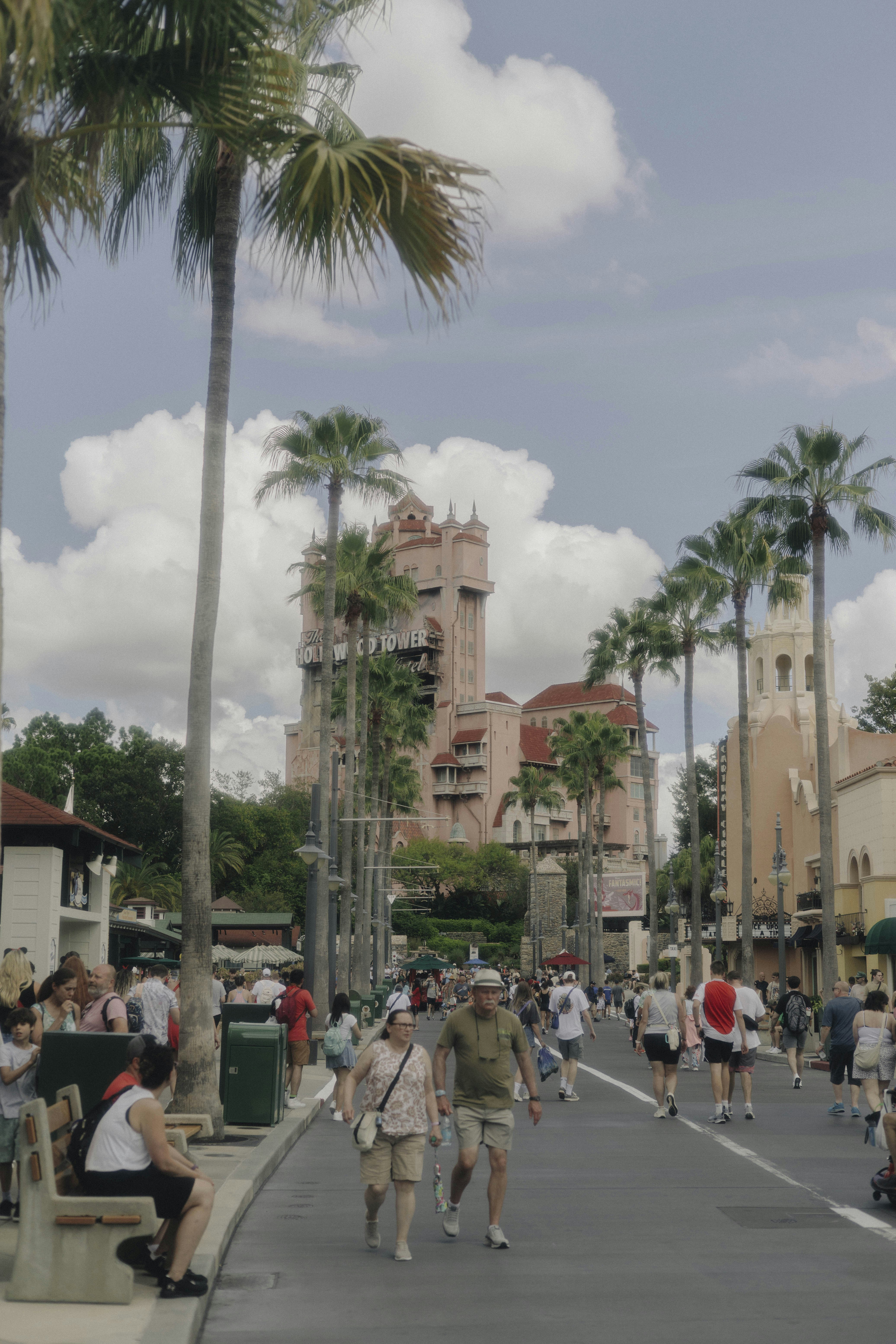 People walk down a street lined with palm trees.