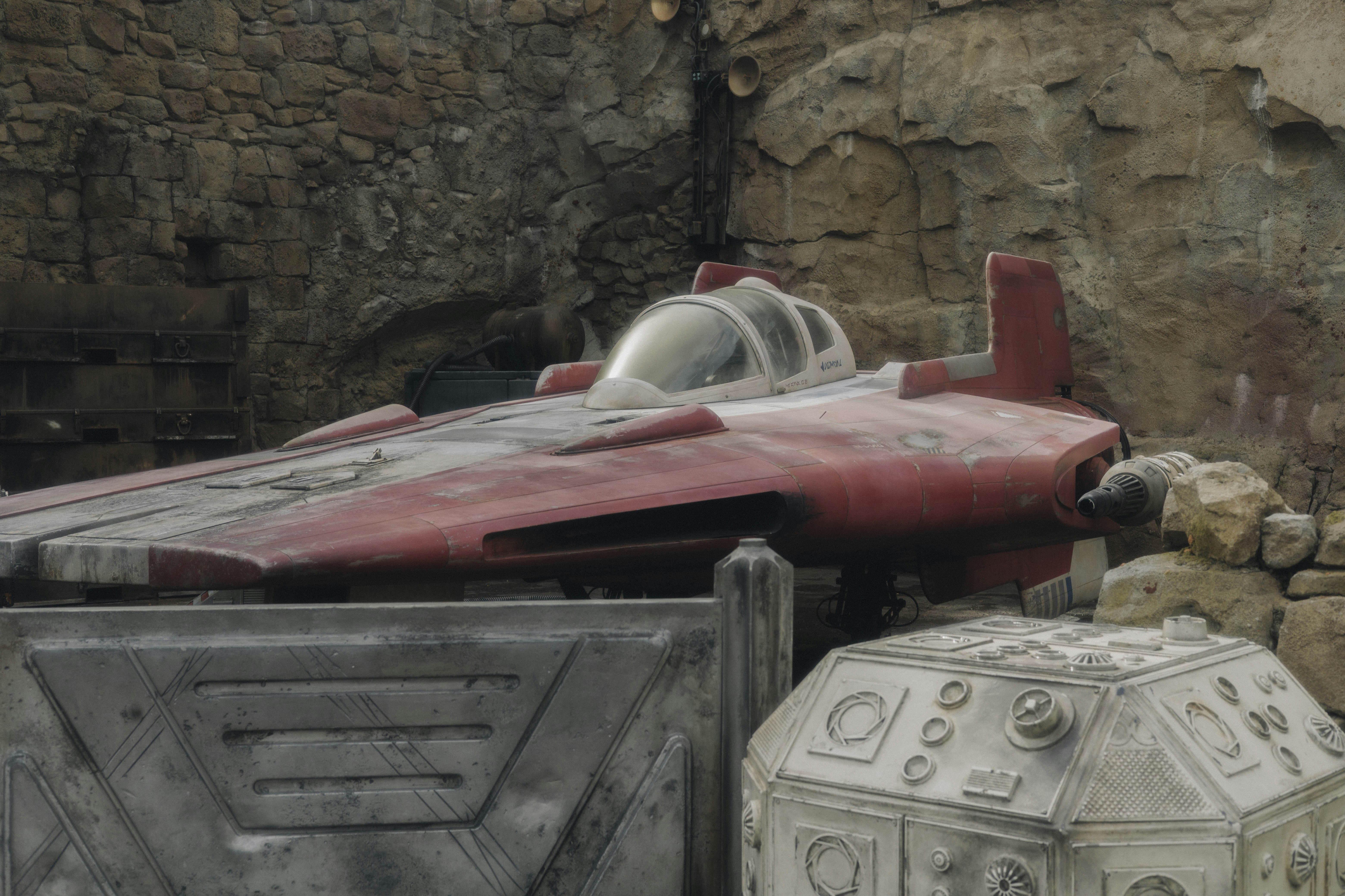 A red and gray spacecraft sits in a rocky area.