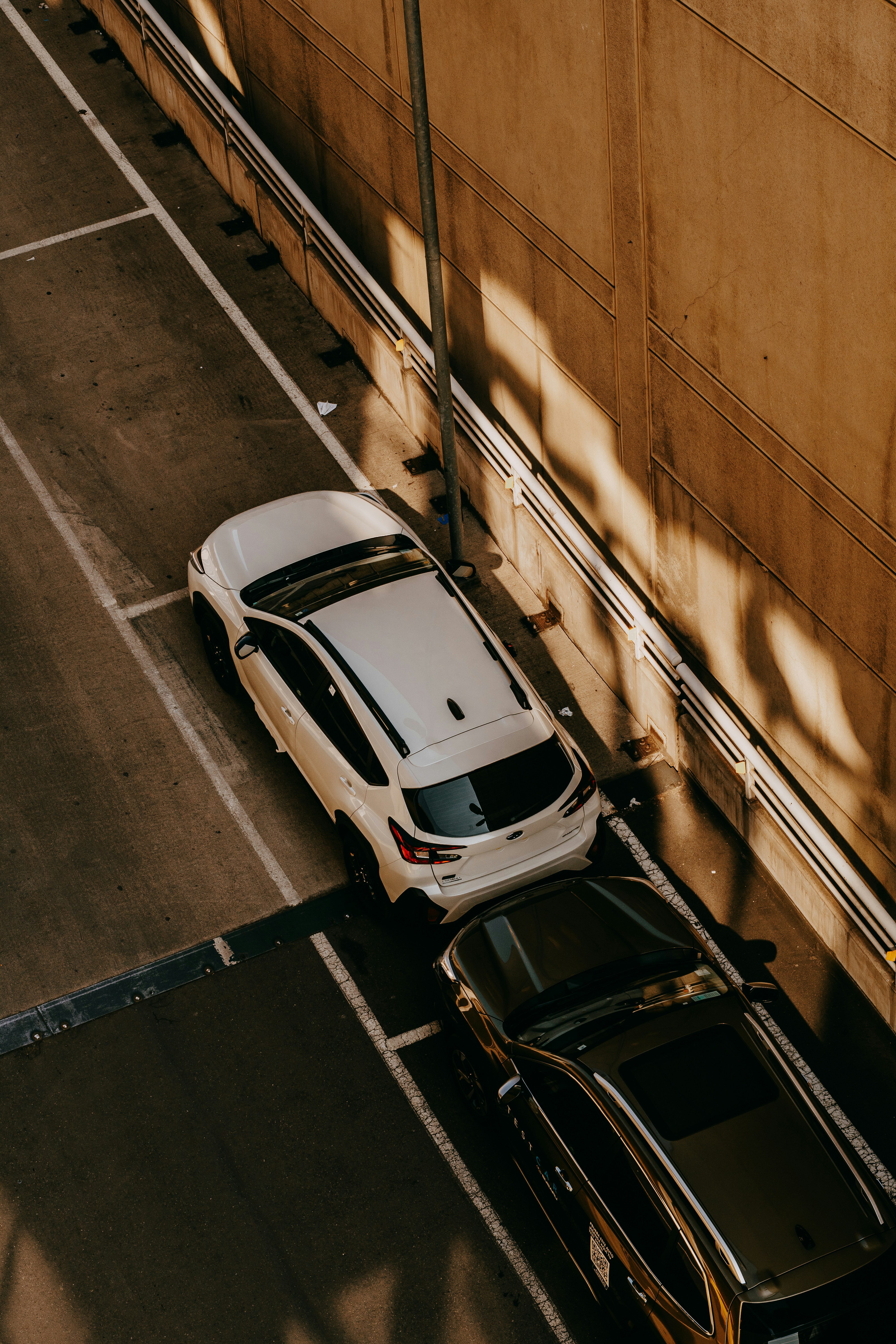 Two cars parked in a lot near a wall.