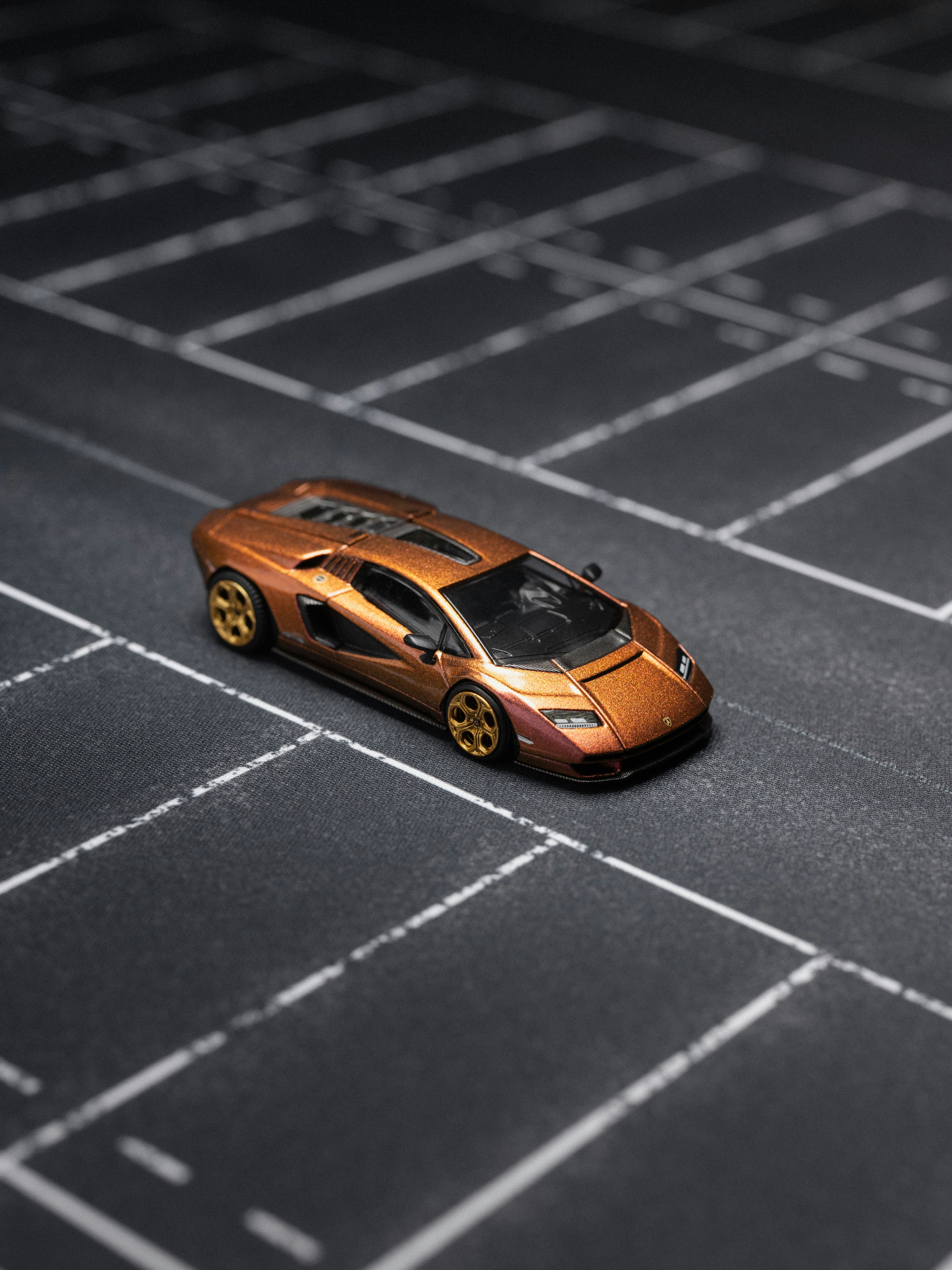 An intricately detailed toy car rests on a stylized parking lot backdrop, showcasing its metallic finish and design features.