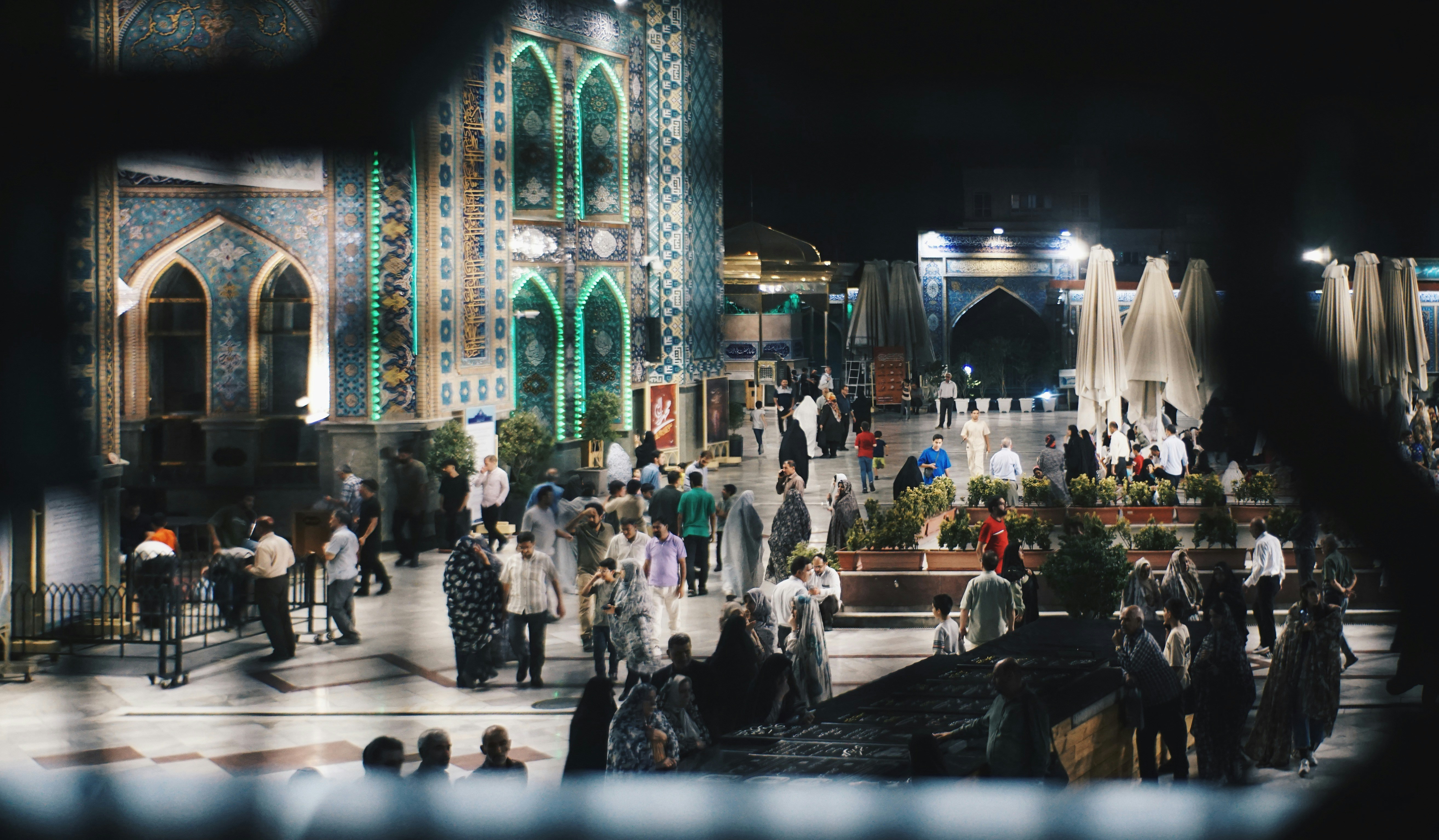 A courtyard alive with faith and fellowship under the night sky. | People gather at a brightly lit mosque at night.