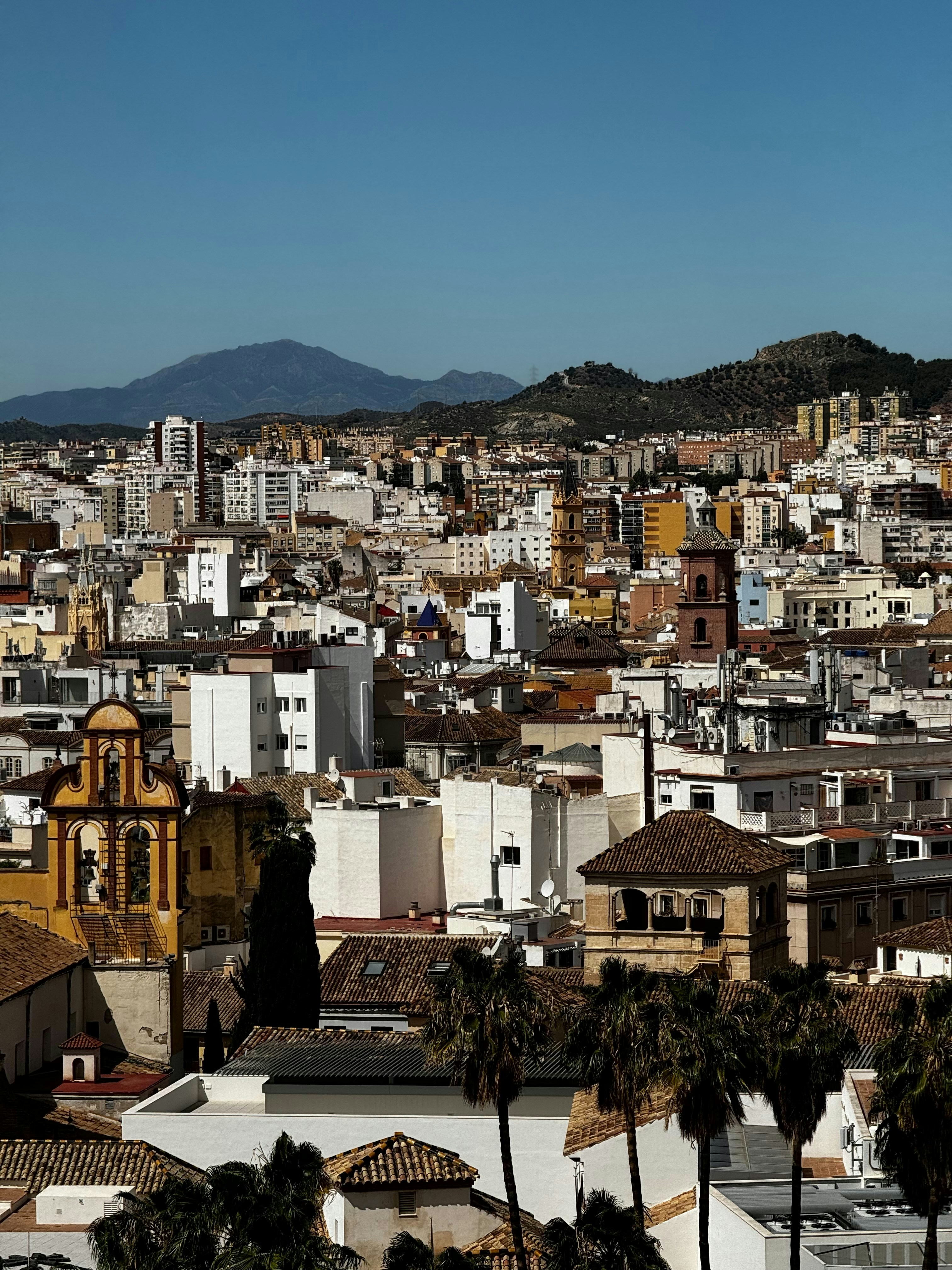 Cityscape with buildings and distant mountains under blue sky.