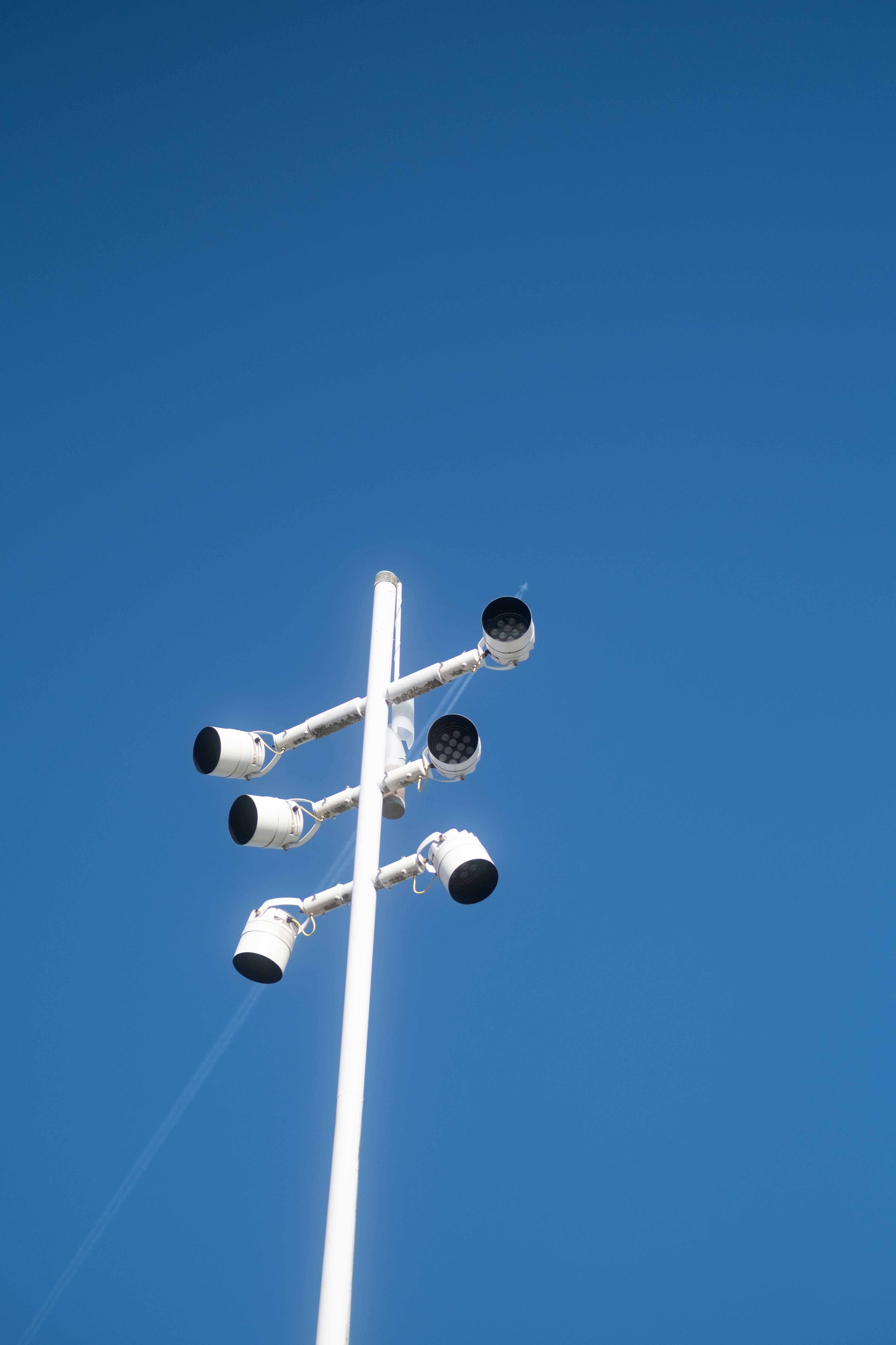 A stadium light with a clear blue sky. | White light pole with multiple spotlights against blue sky