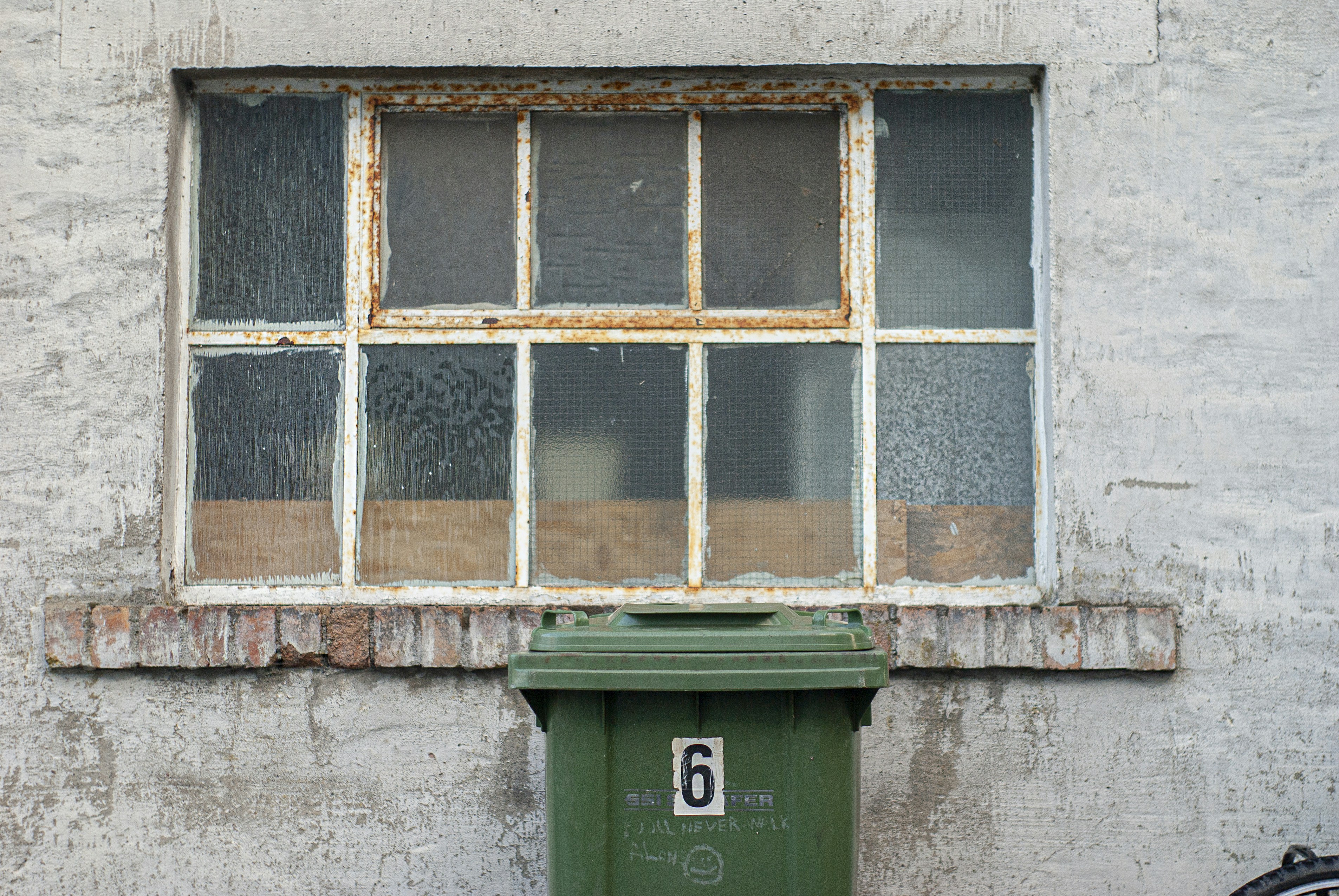 SONY DSC | Green trash bin in front of a weathered window.