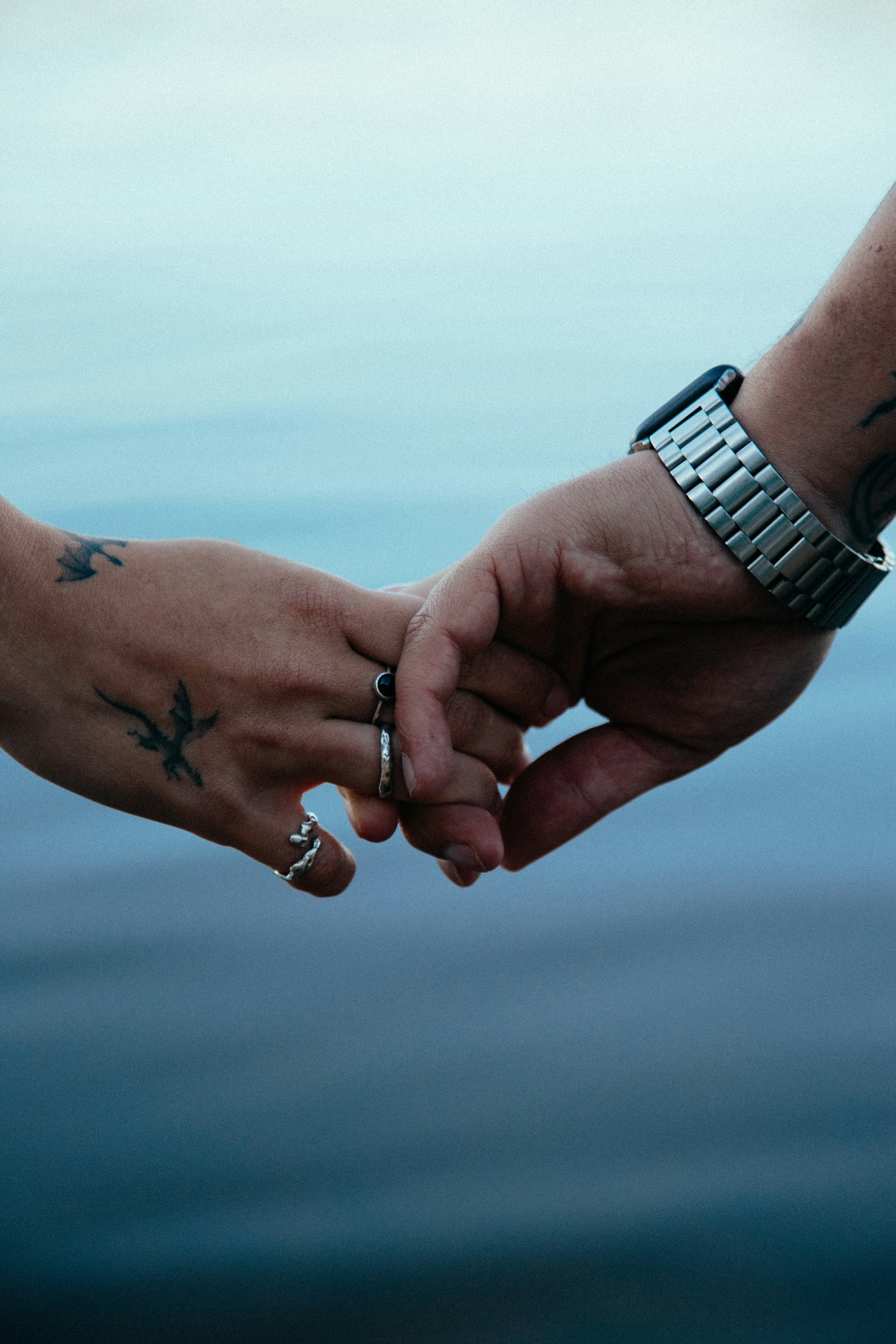 Couple holding hands with tattoos and rings.