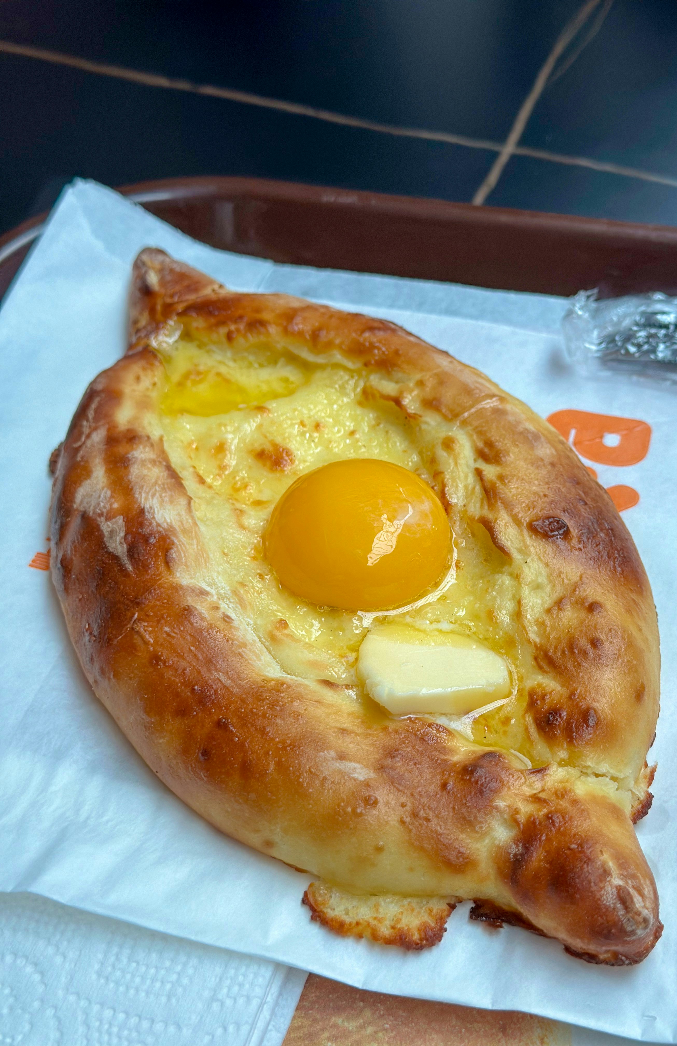 Khachapuri a traditional georgia foods, half cooked egg on top of a bread. | Khachapuri with egg and butter on white paper.