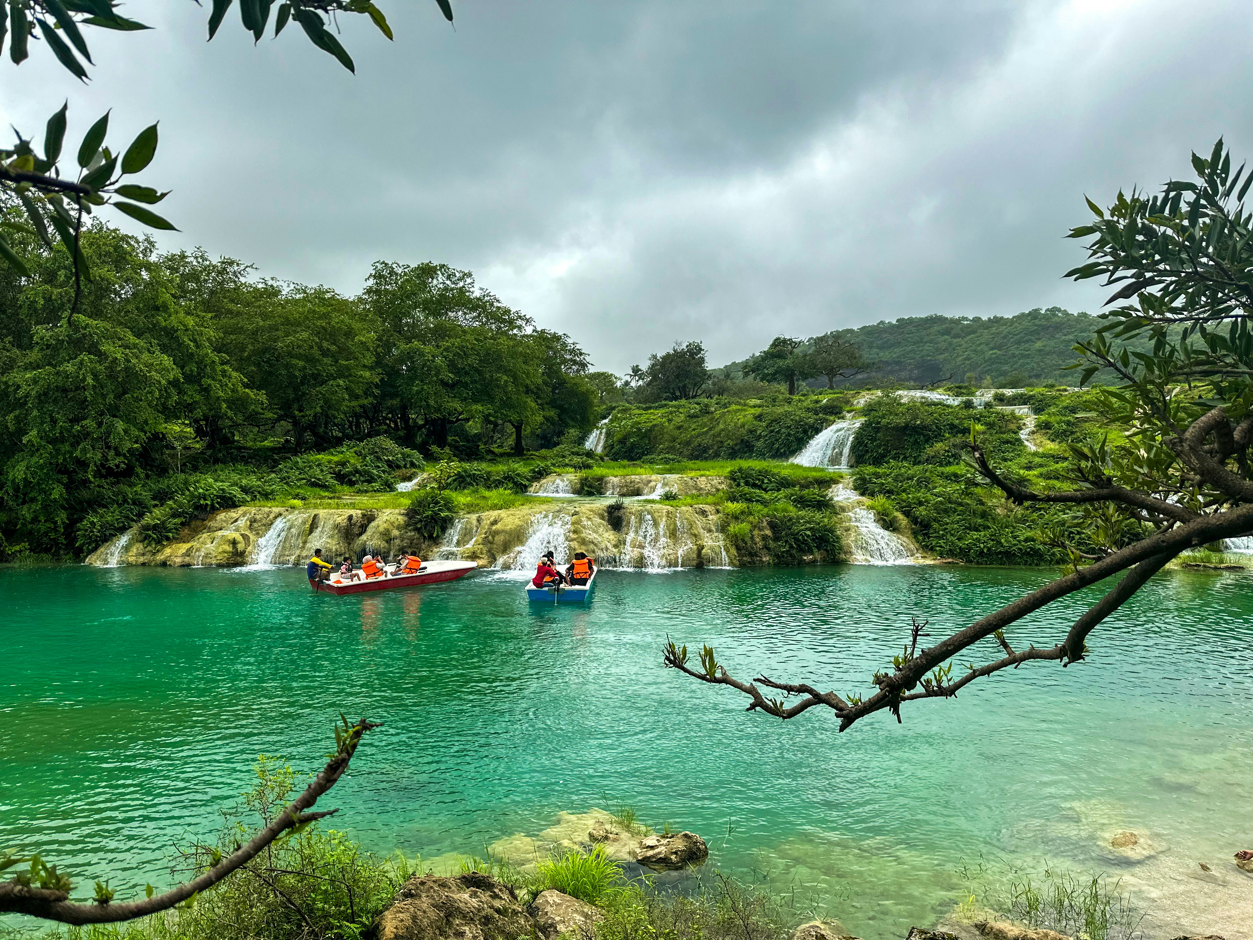a beautiful lake a tourist attraction in salalah. | Boats on a turquoise lake with cascading waterfalls.