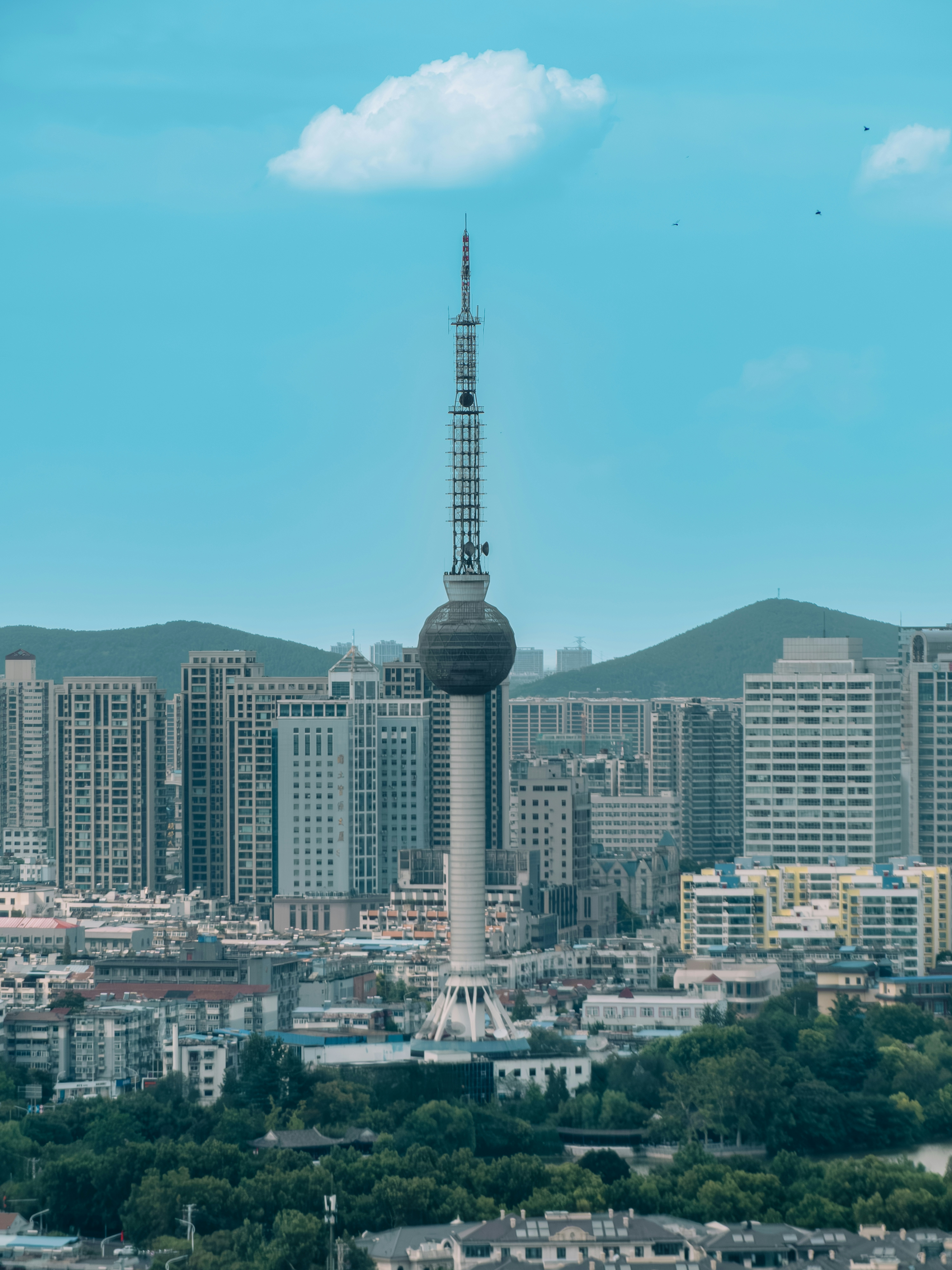 A towering observation tower rises amidst a bustling urban landscape, showcasing modern architecture against a clear blue sky.
