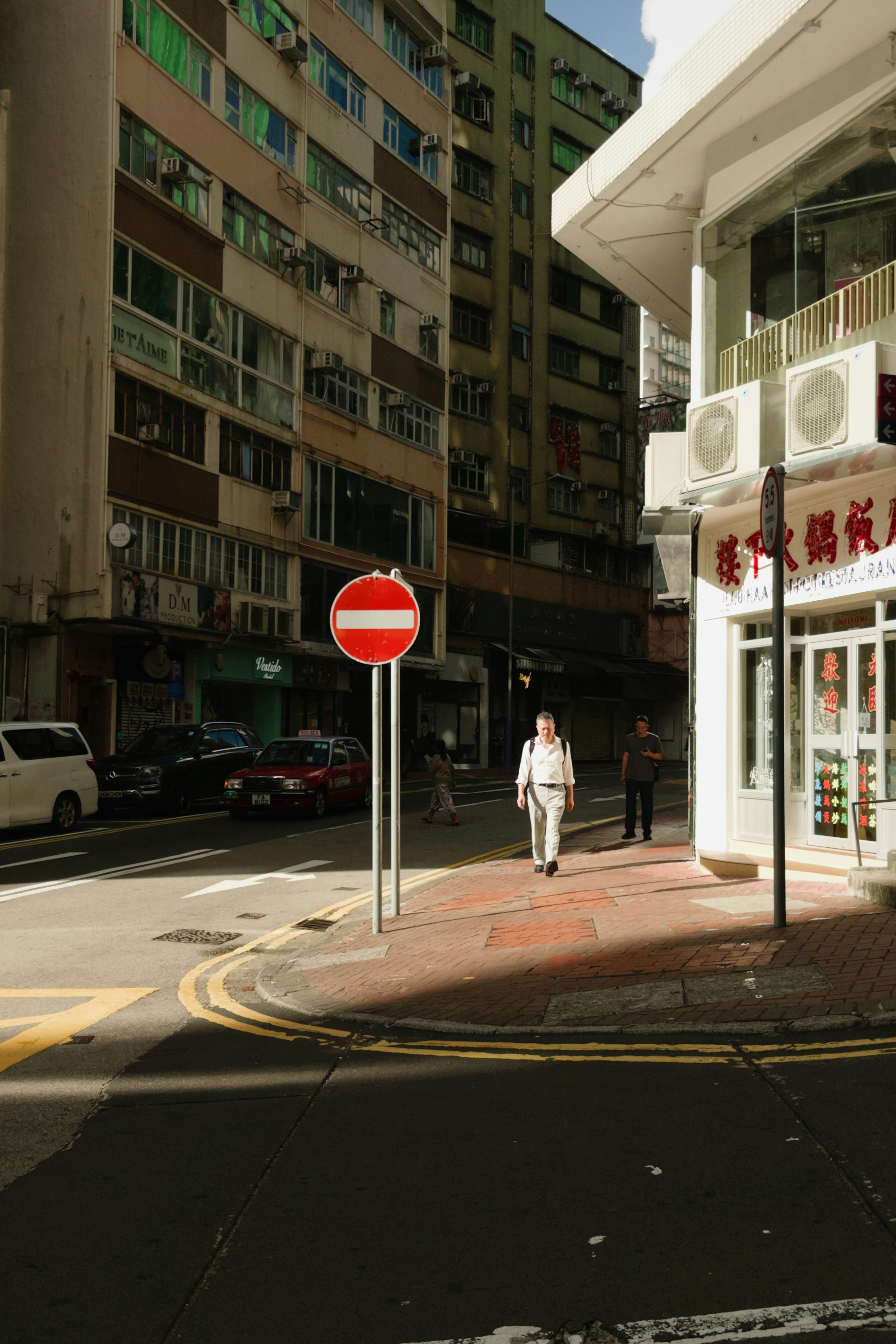 man on the streets of Hong Kong | Man walks down sunlit city street with buildings.