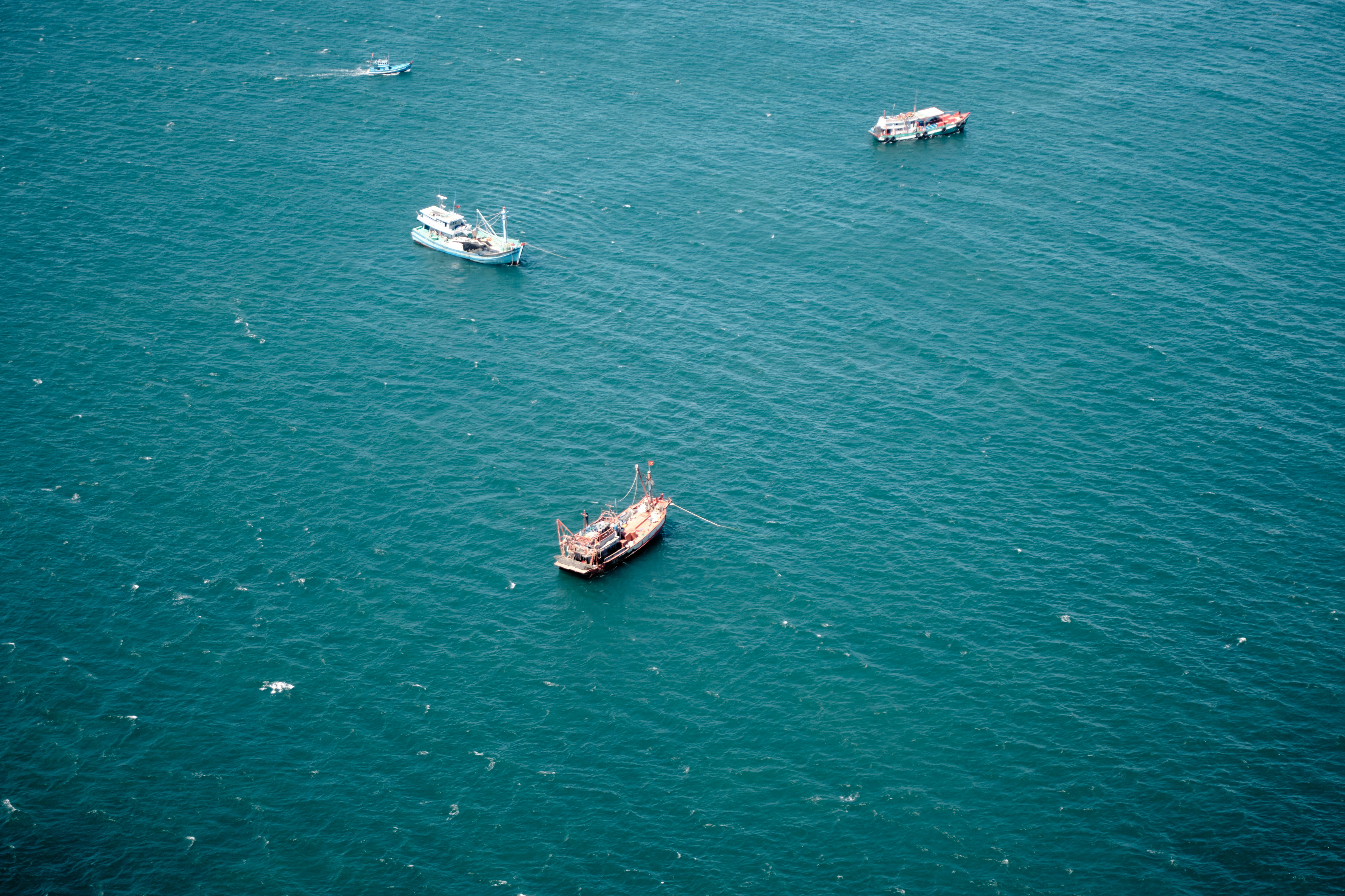 Teal Expanse: An Aerial View of Three Boats on a Quiet Sea