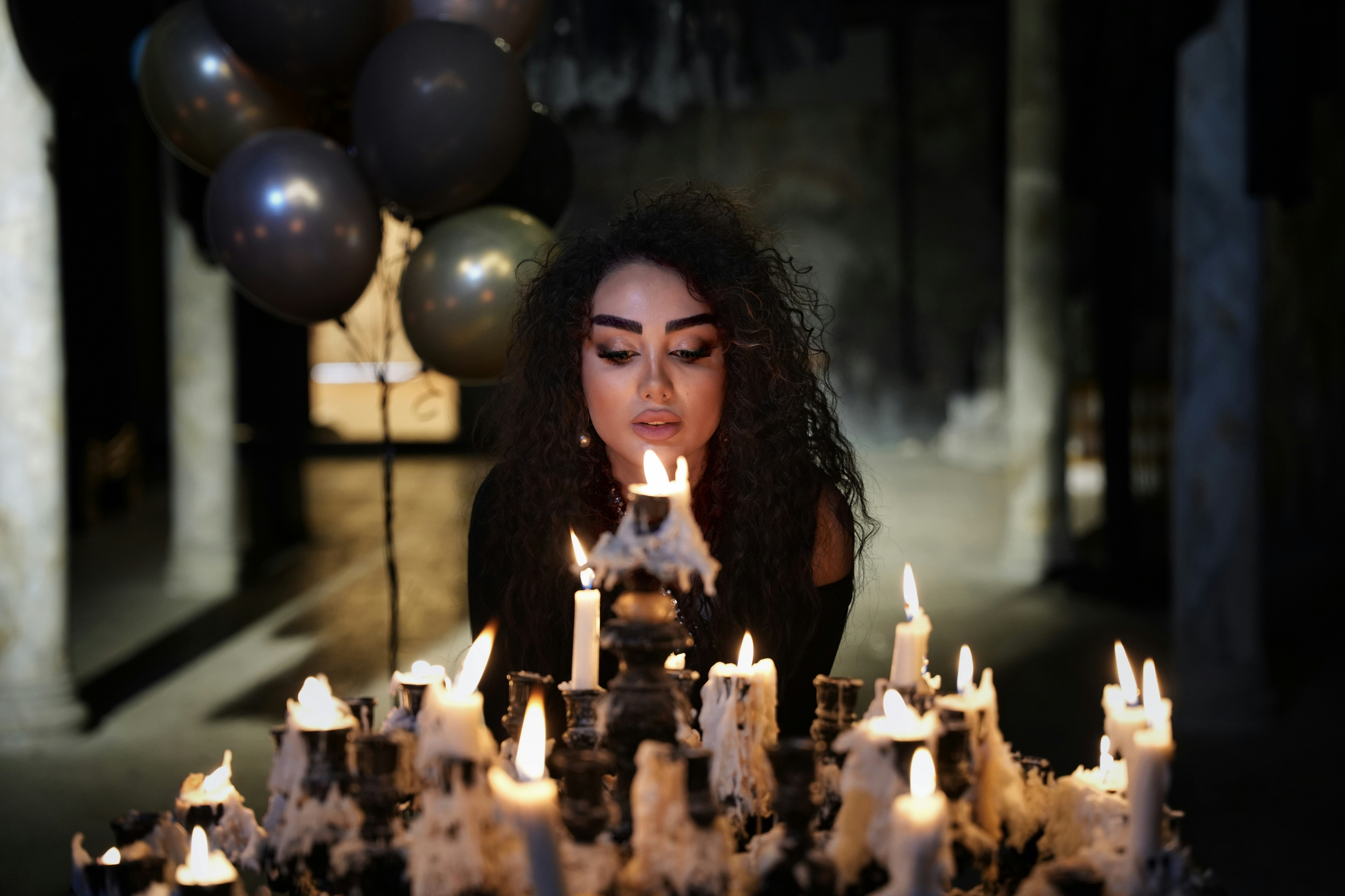 Woman blowing out candles with balloons behind her.
