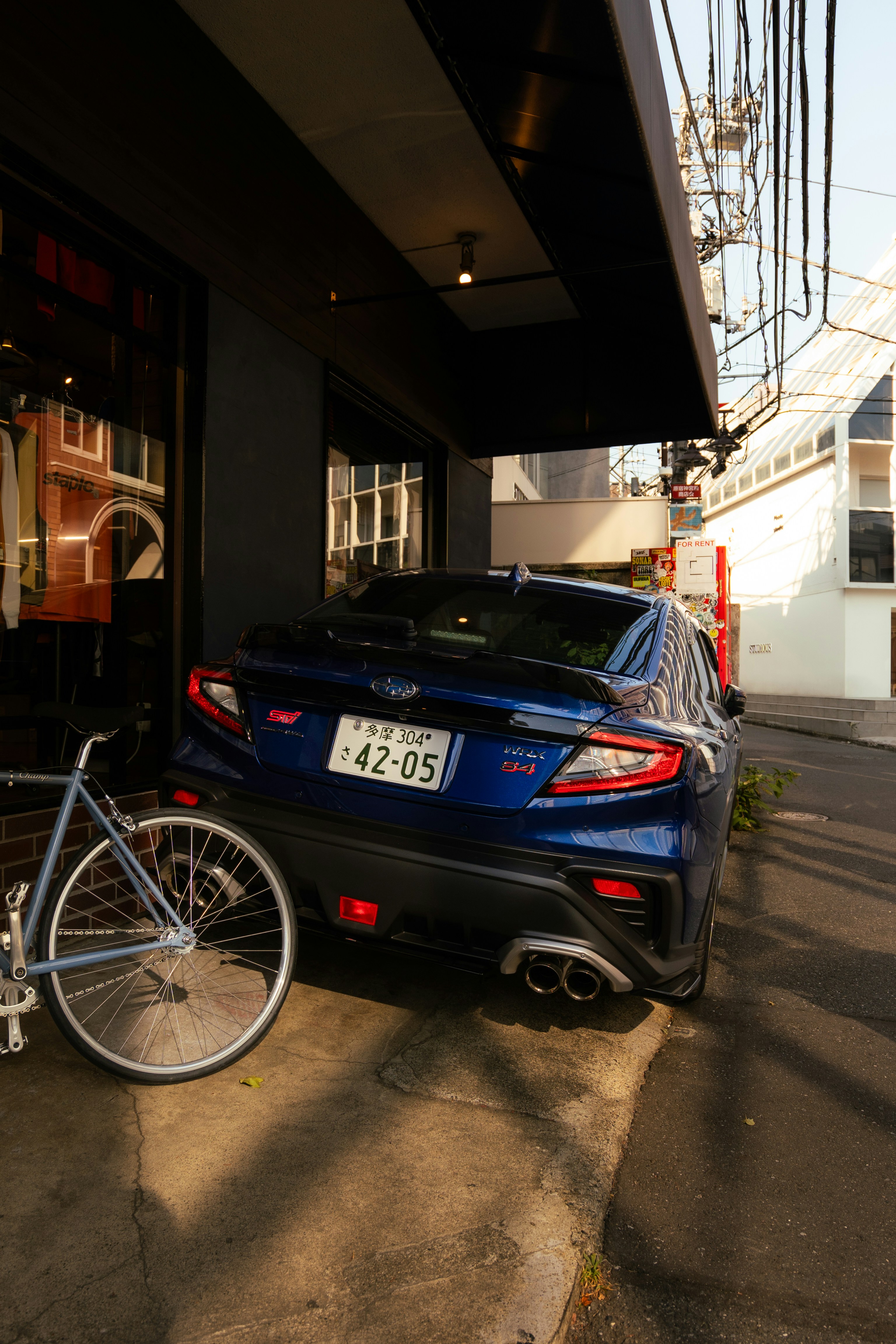 Blue car parked by a storefront with a bicycle.