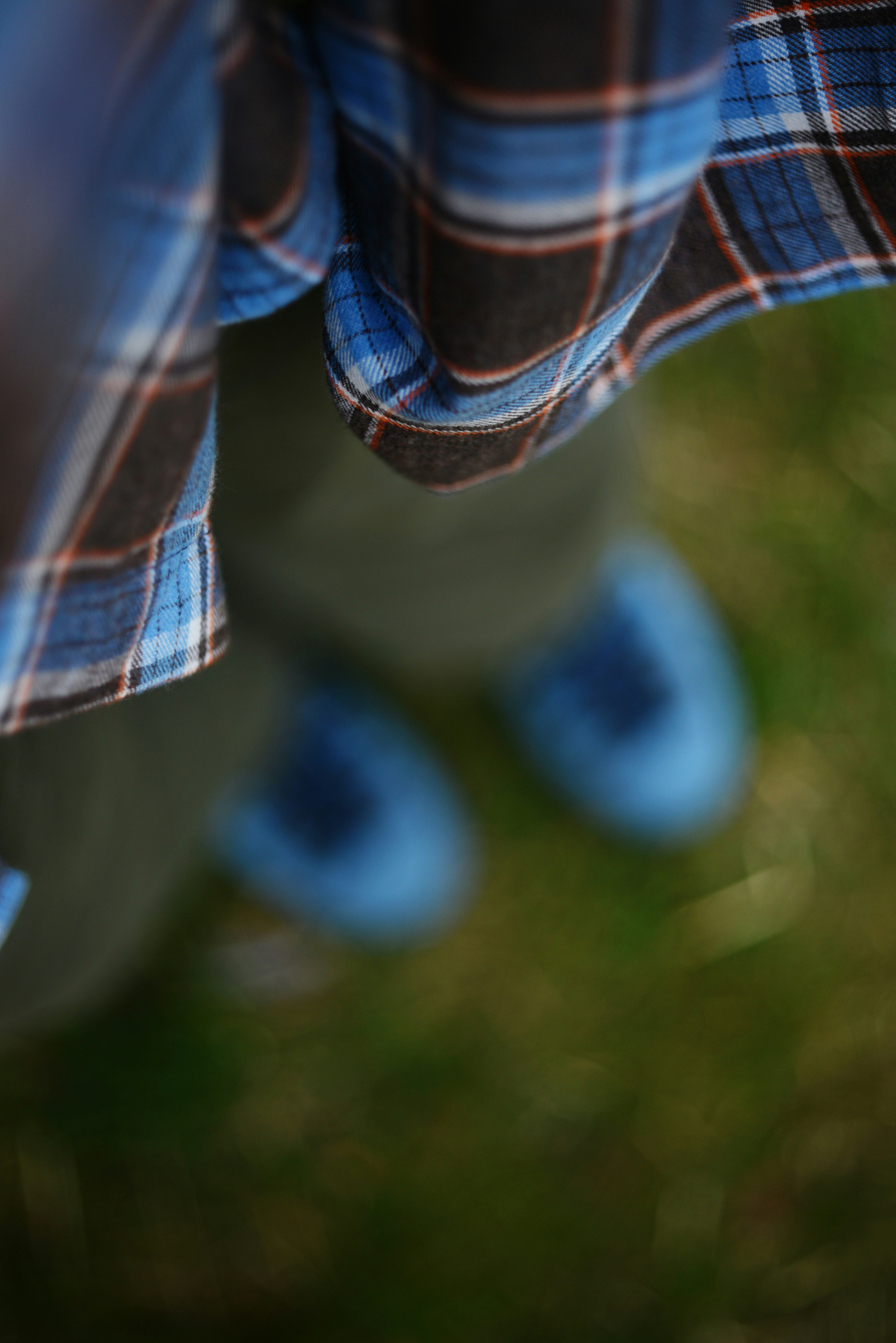 Close-up of a plaid shirt and blue shoes against a grassy background, emphasizing a relaxed outdoor moment.