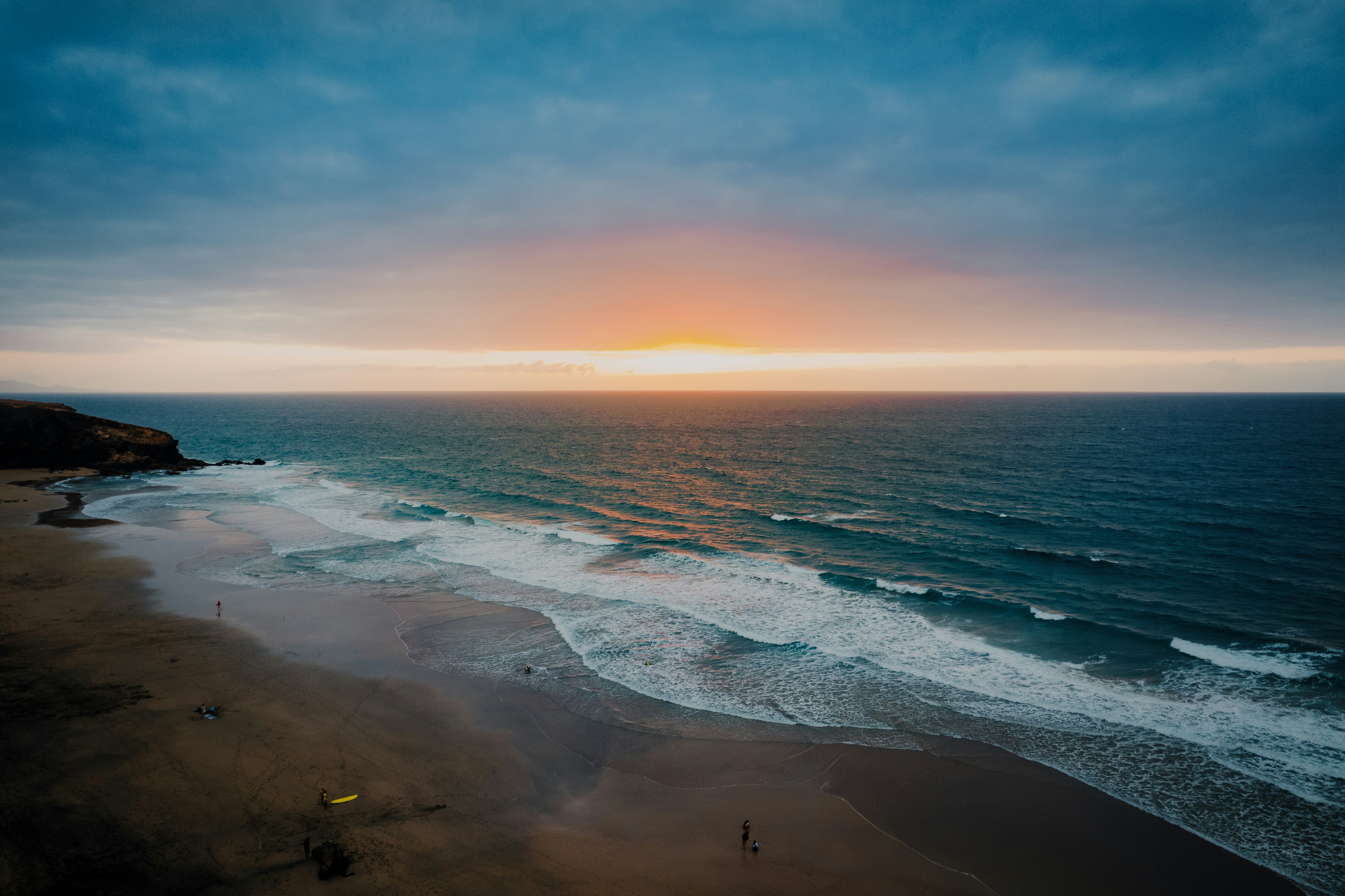 Sunset over a calm ocean with waves on beach.