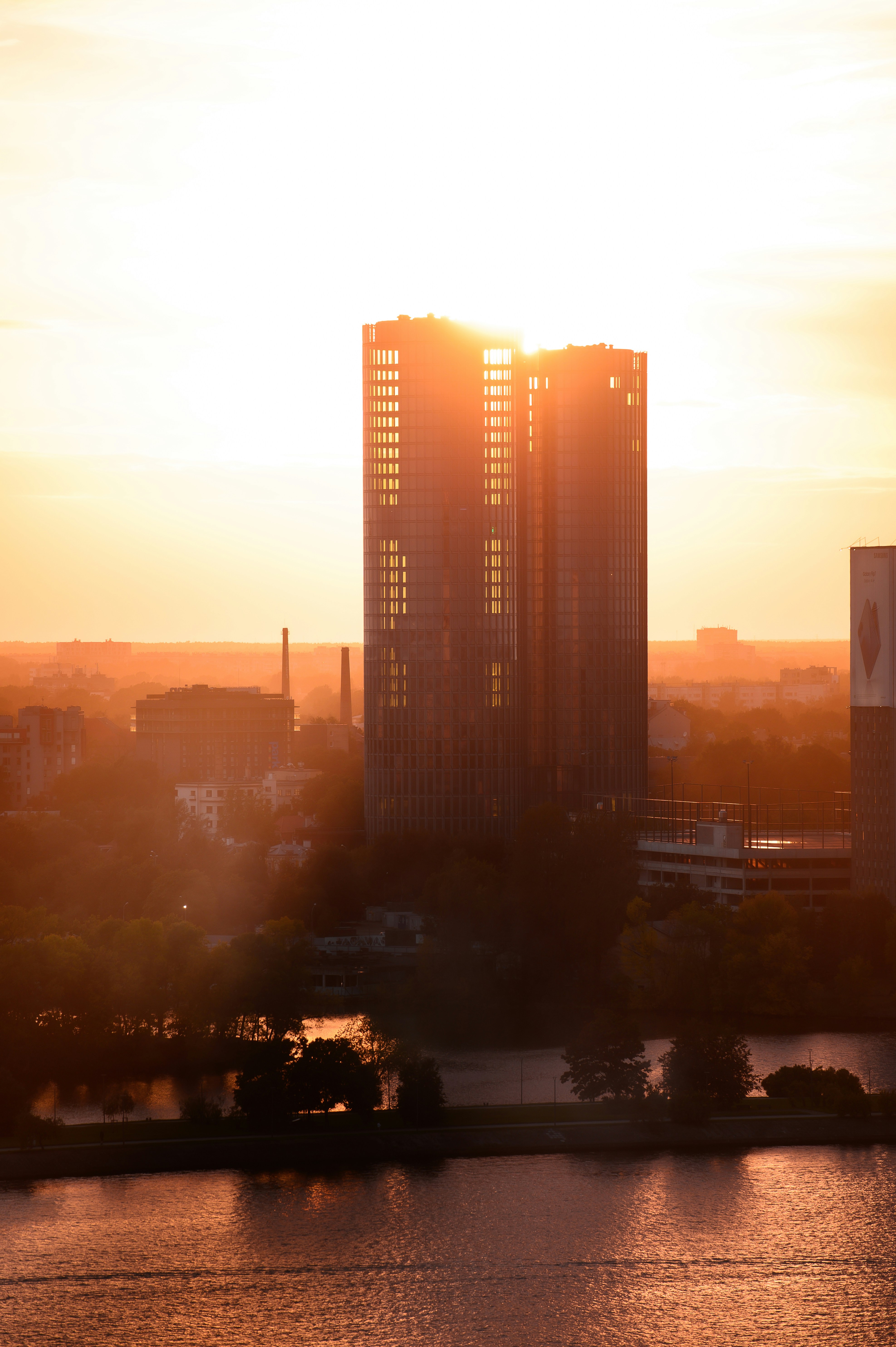 Two towering skyscrapers illuminated by the setting sun, casting reflections on the water below. The scene captures the essence of urban life transitioning into evening.