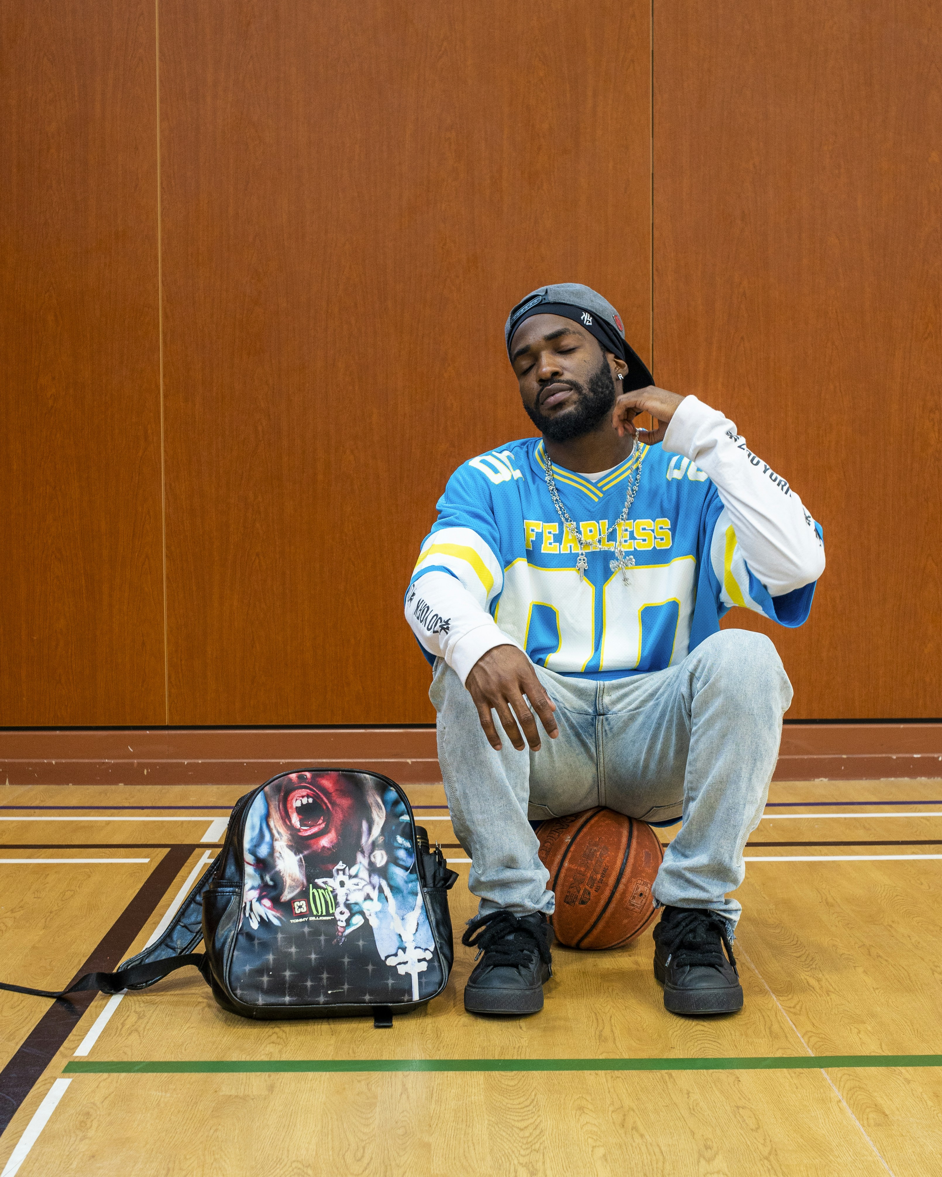Man in basketball jersey sits on ball with backpack.