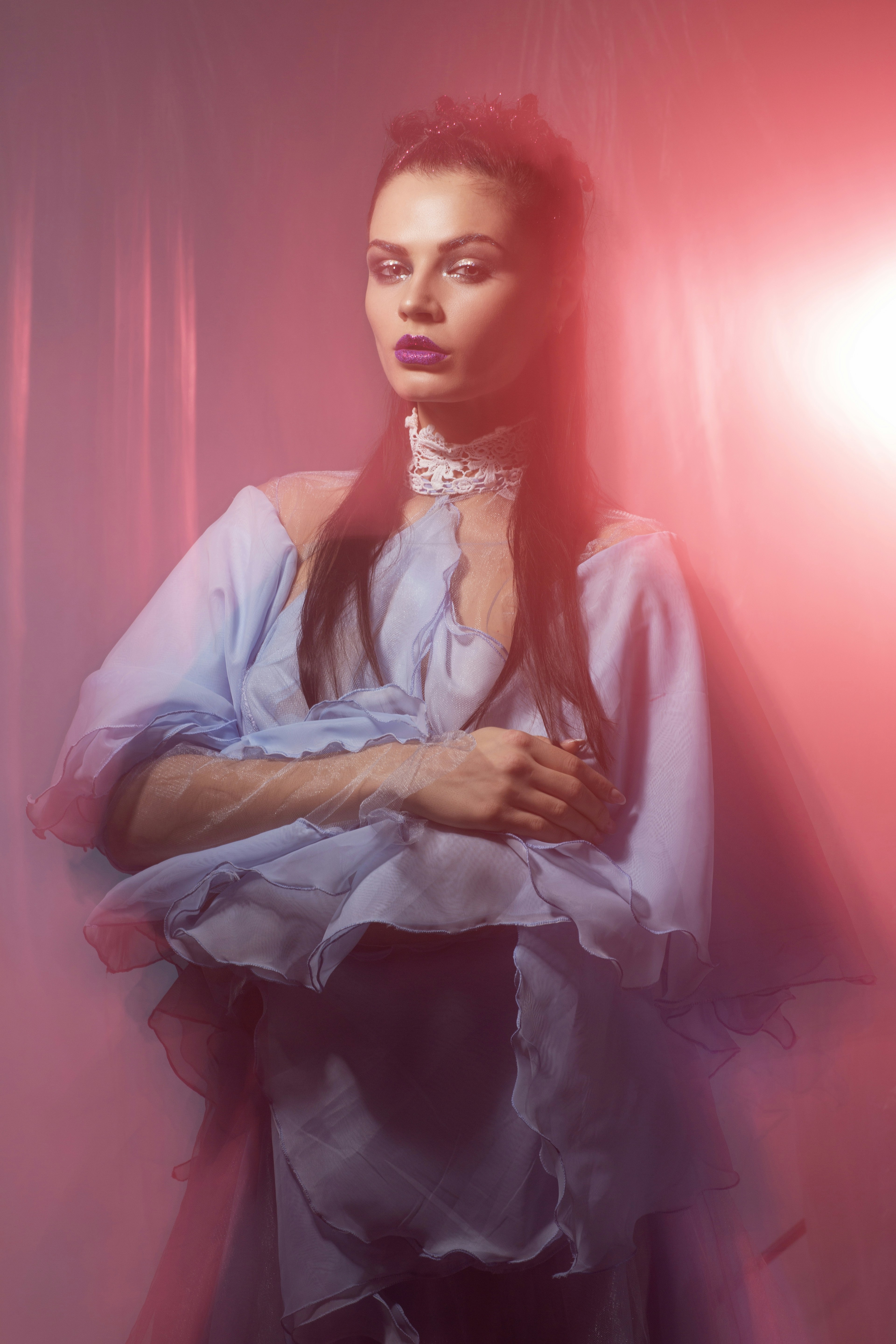 A model adorned in a flowing, translucent blue garment stands against a softly lit backdrop, exuding a serene yet striking presence.