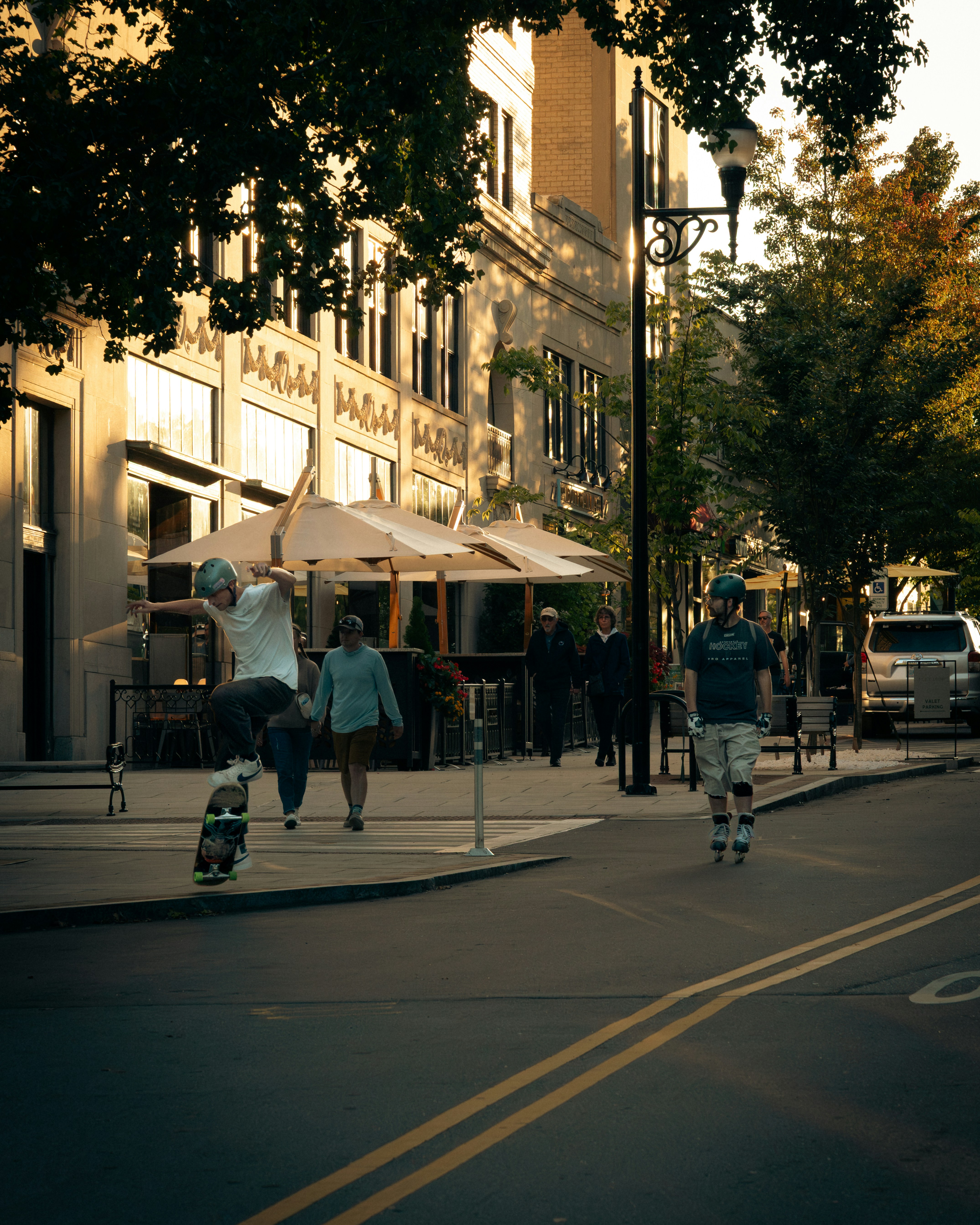 Urban street photography with people in city life | Skateboarder performs trick on city street with rollerblader nearby.