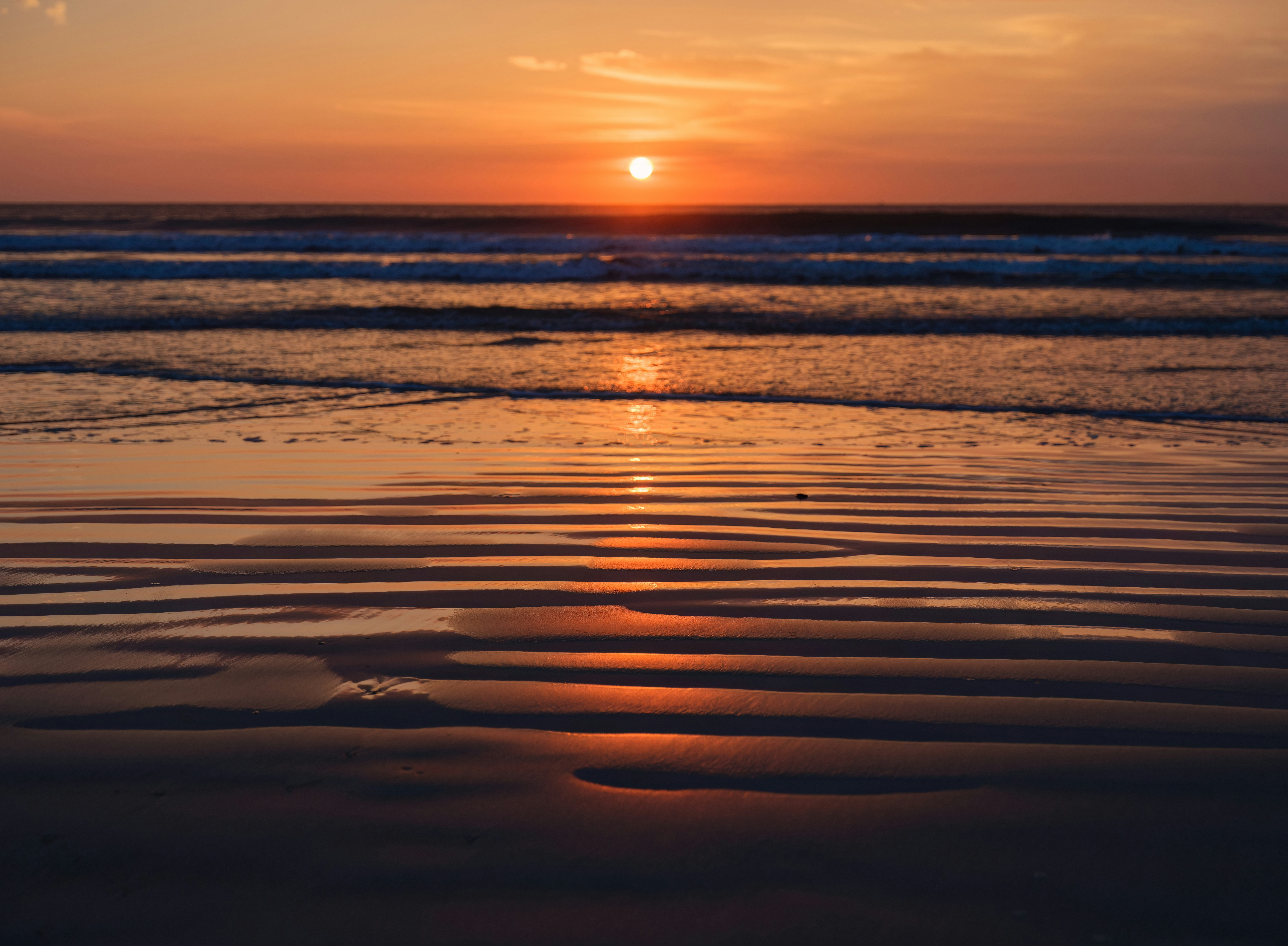 Sunset over a calm ocean with wet sand ripples