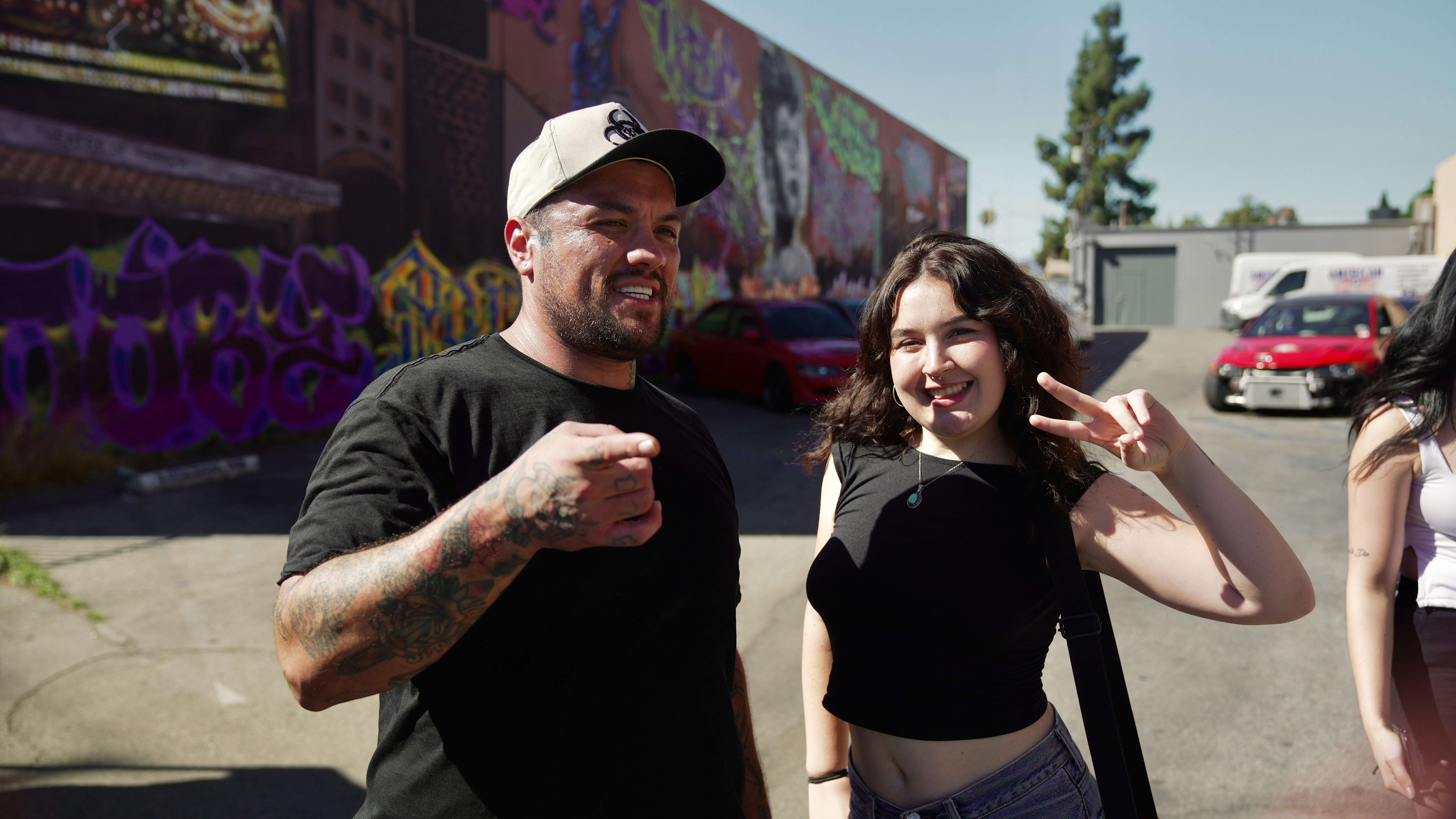 Two friends posing playfully in front of vibrant street art, showcasing a lively urban atmosphere.