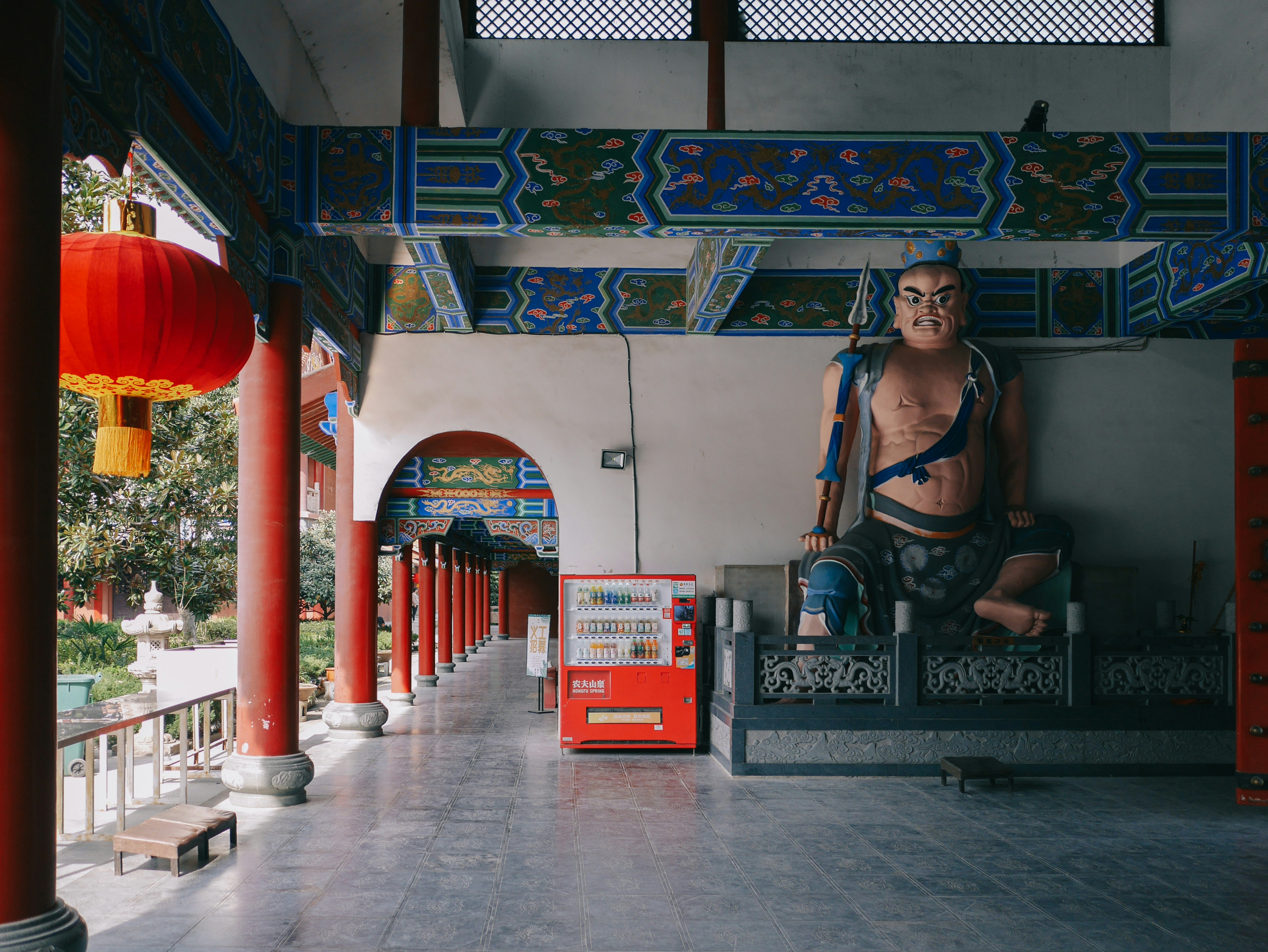 Ornate temple hallway with statue and red lantern.