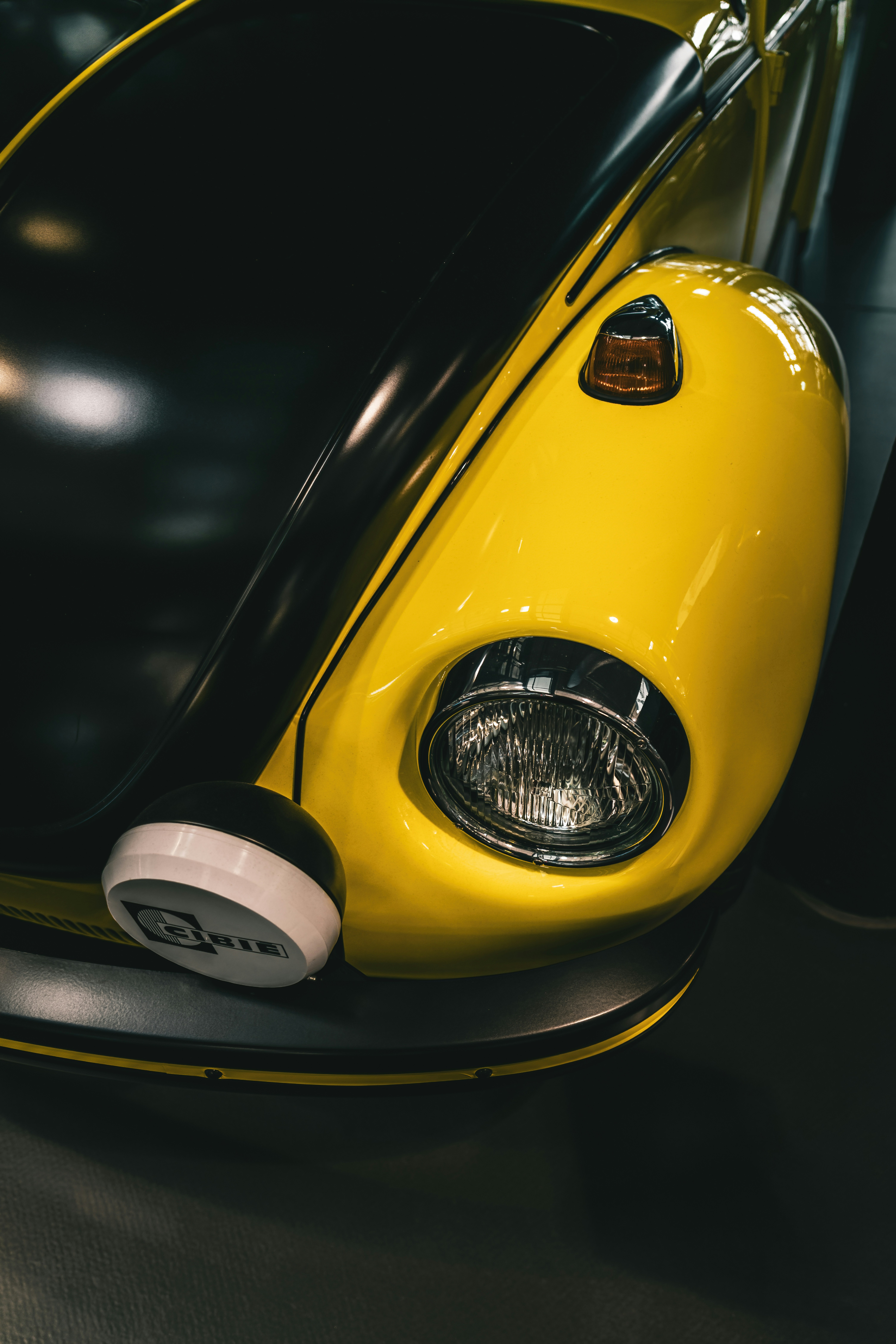 Close-up of a vintage yellow car showcasing its unique headlight and sleek curves. The blend of colors highlights the vehicle's classic design.
