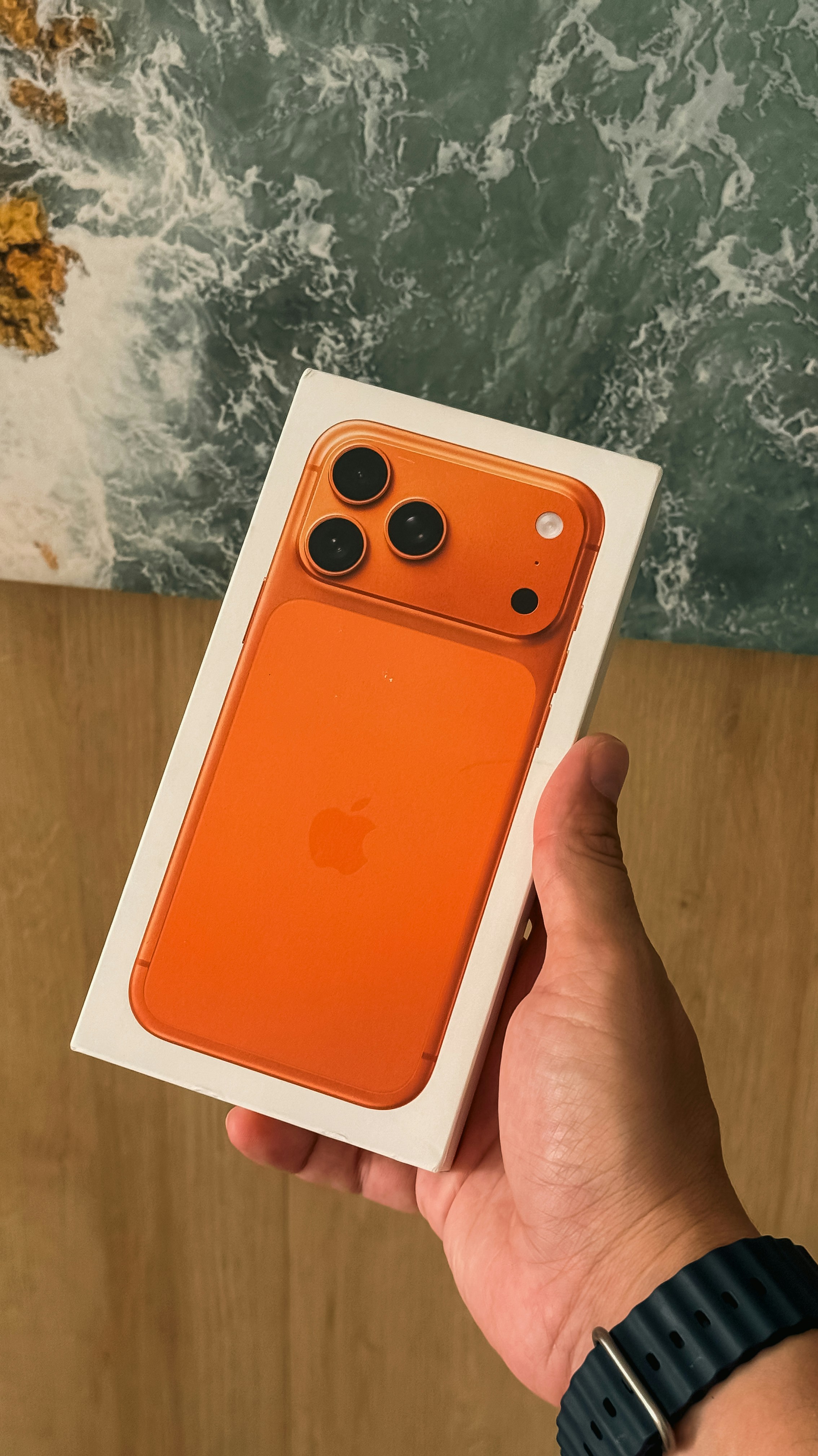 Hand holding orange iPhone box with artistic background