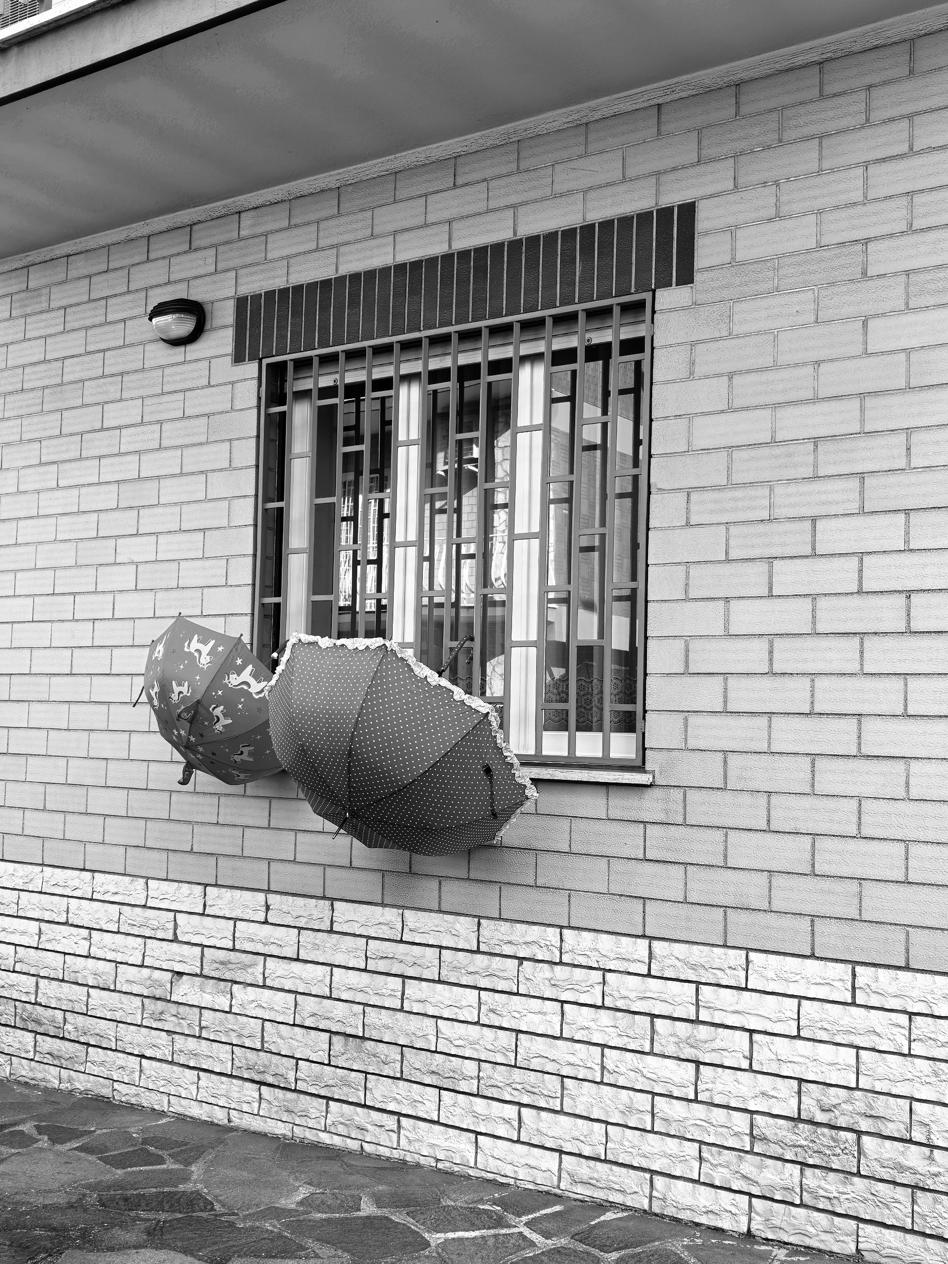 Two umbrellas hang on a barred window.