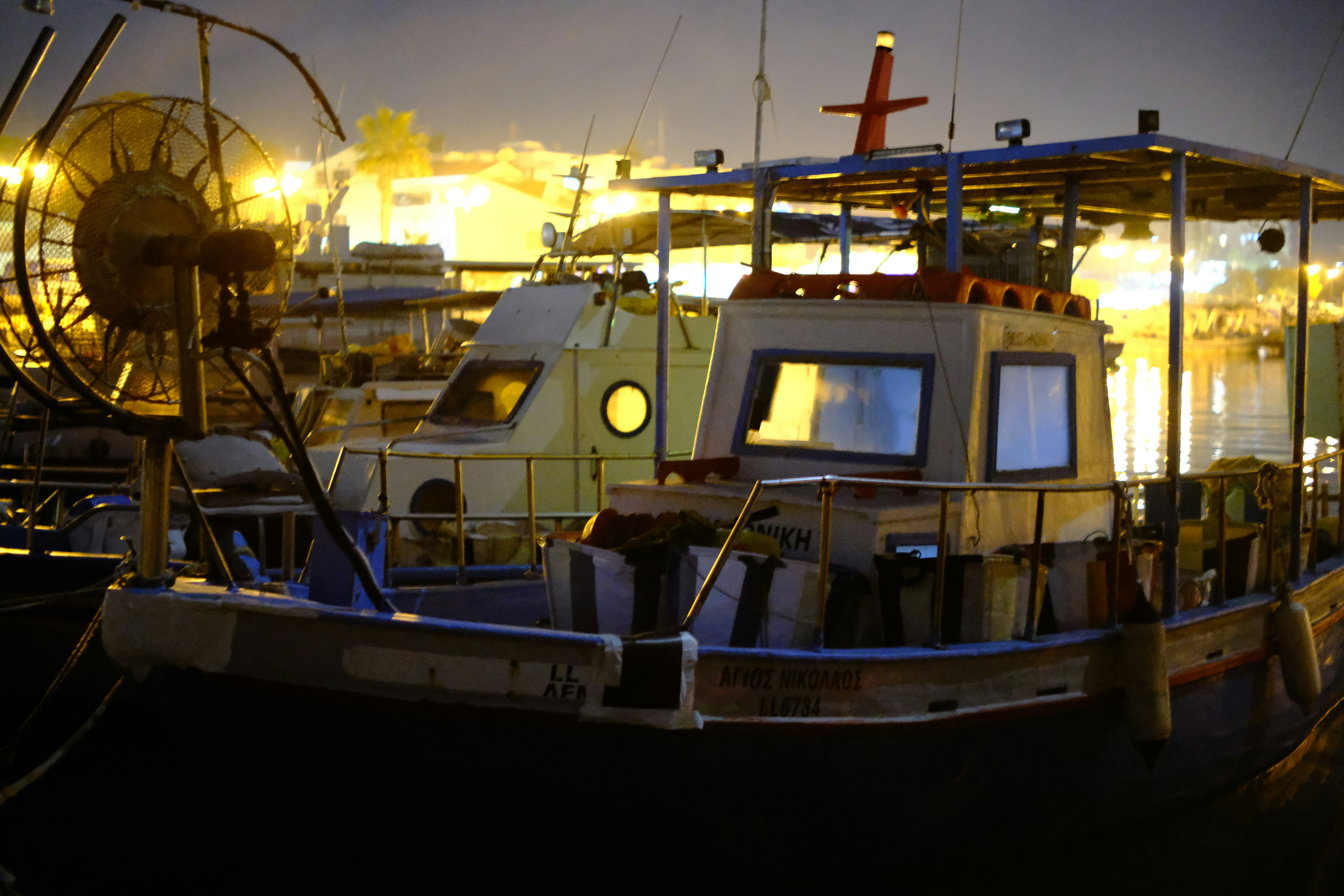 Fishing boats docked in a harbor illuminated by ambient city lights at night.